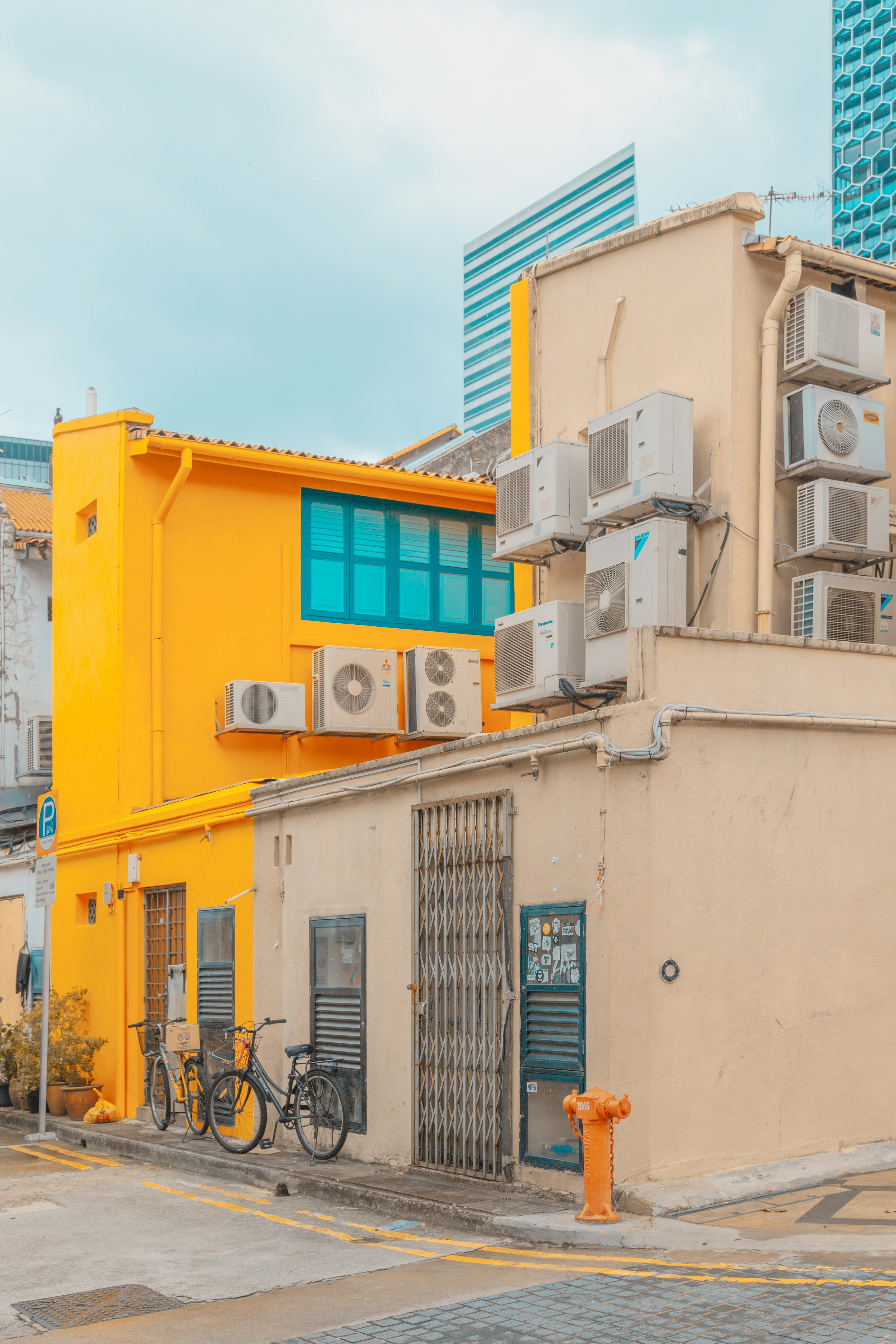 Sunlit Yellow Facade with Aqua Windows and HVAC Towers on a Quiet Urban Corner