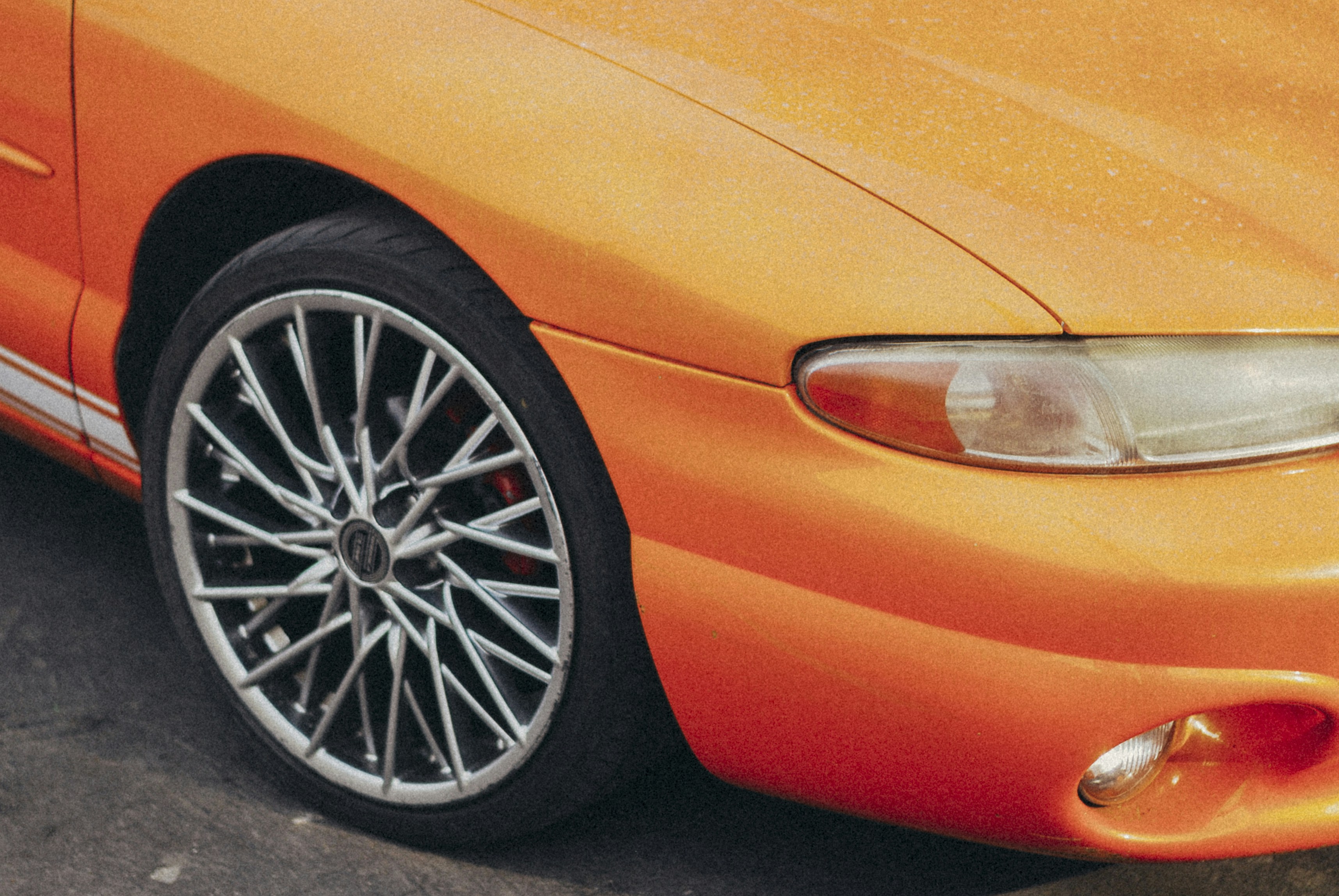Close-up of a striking orange car showcasing its sleek wheel design and glossy finish.