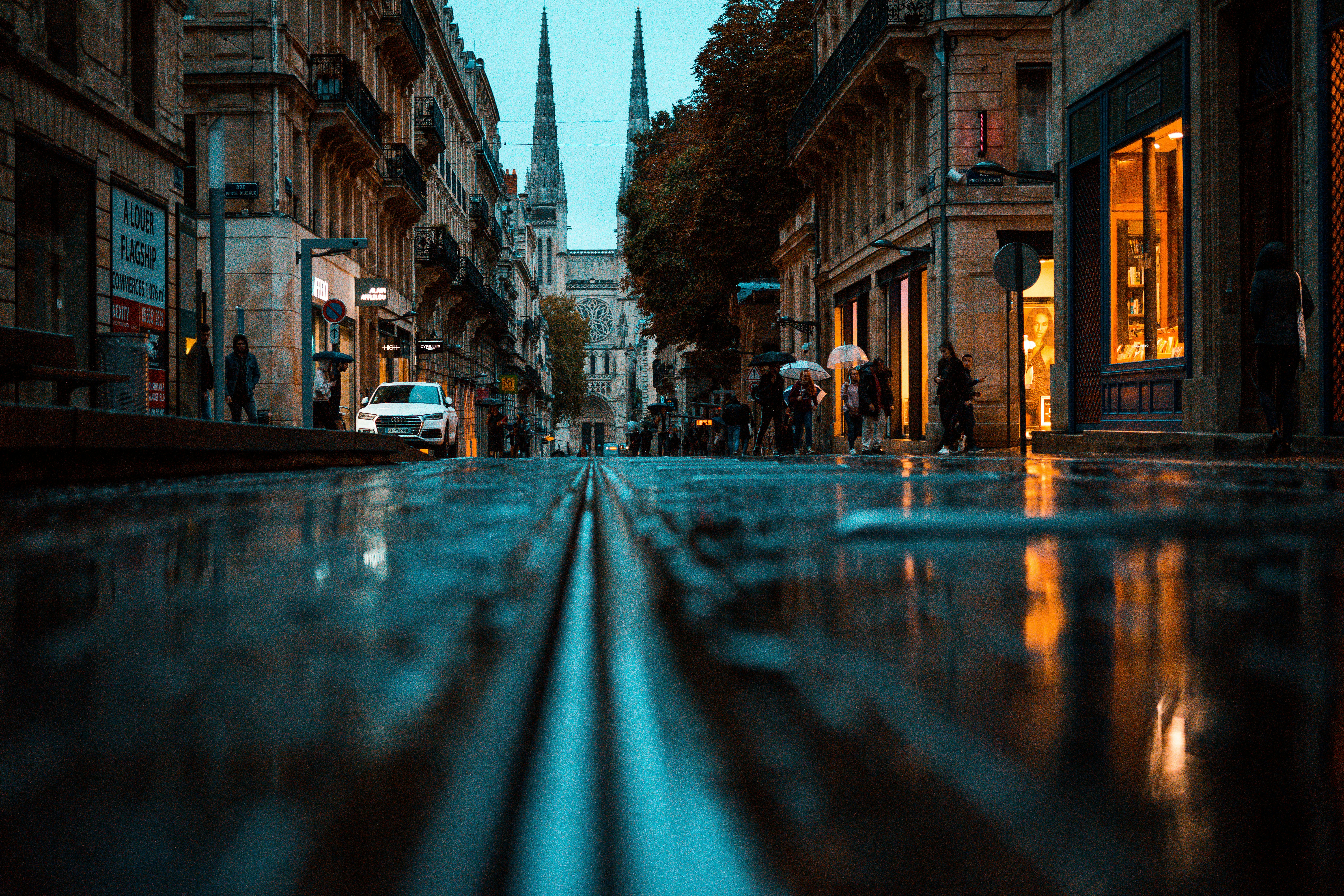 Wet cobblestone street reflecting city lights and spires in the distance, creating a moody urban atmosphere.