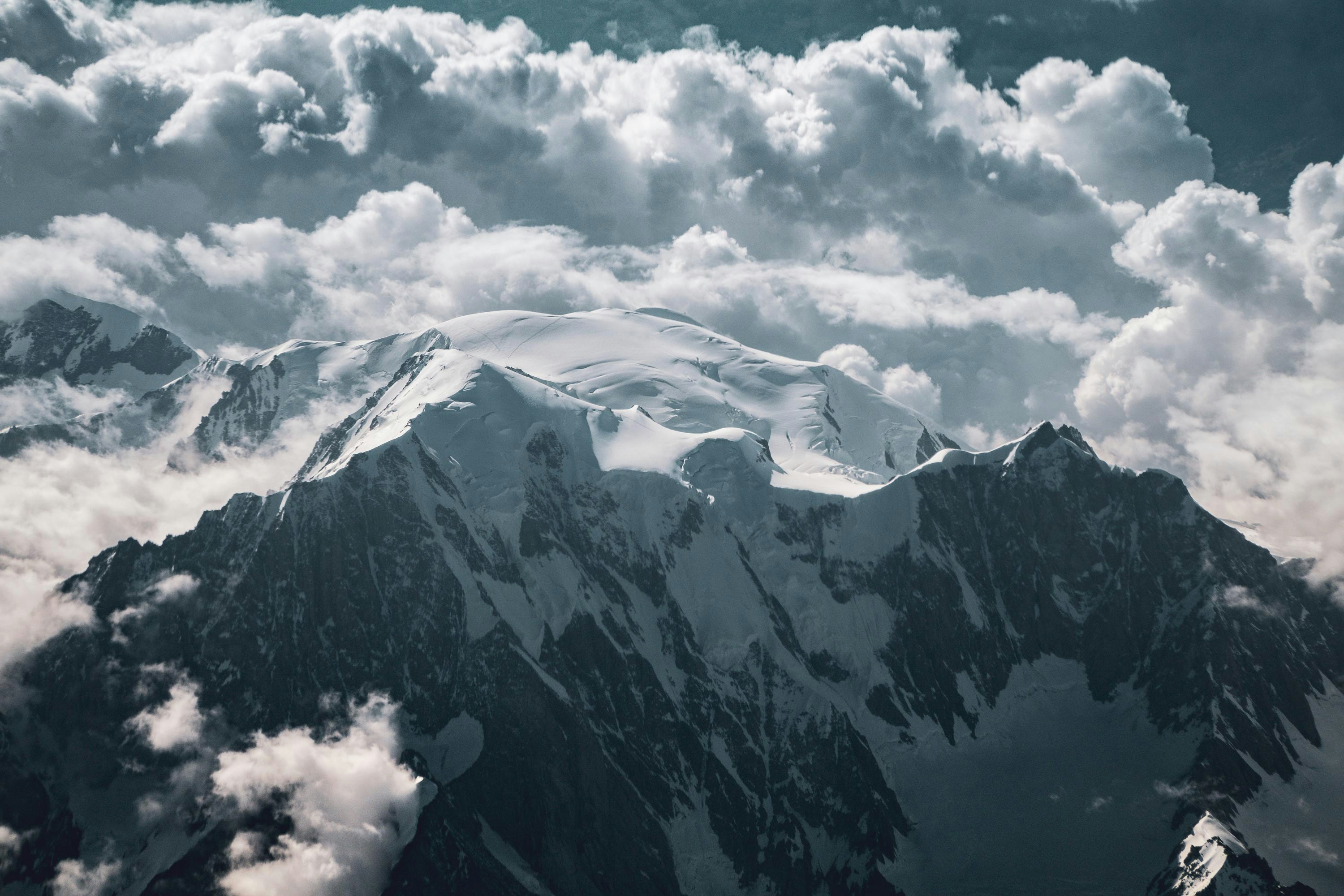 Snow-covered mountain summit surrounded by dramatic clouds under a vibrant sky.