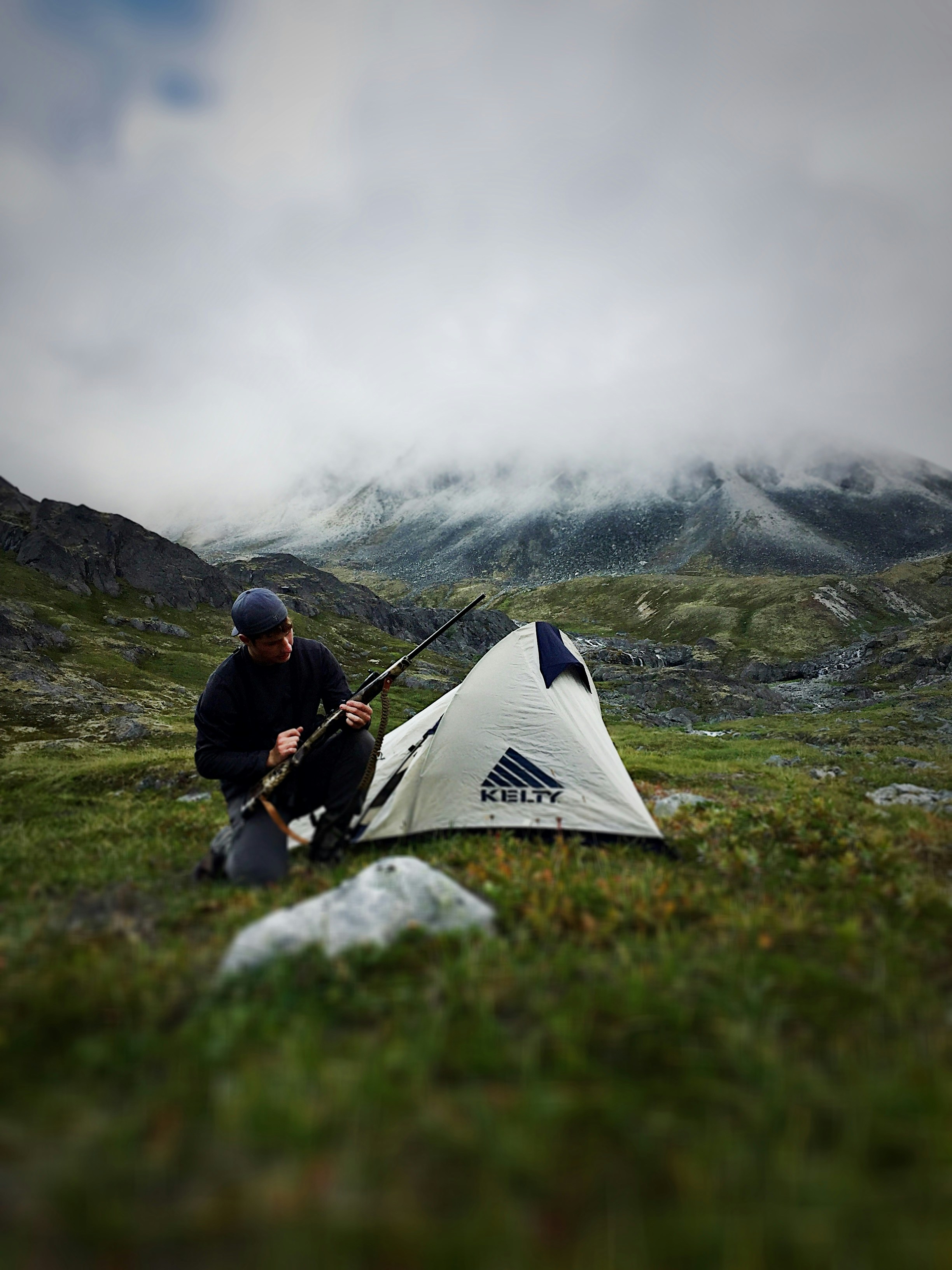 Alpine Patience Beneath Mist: A Camper Tends Gear by a Kelty Tent
