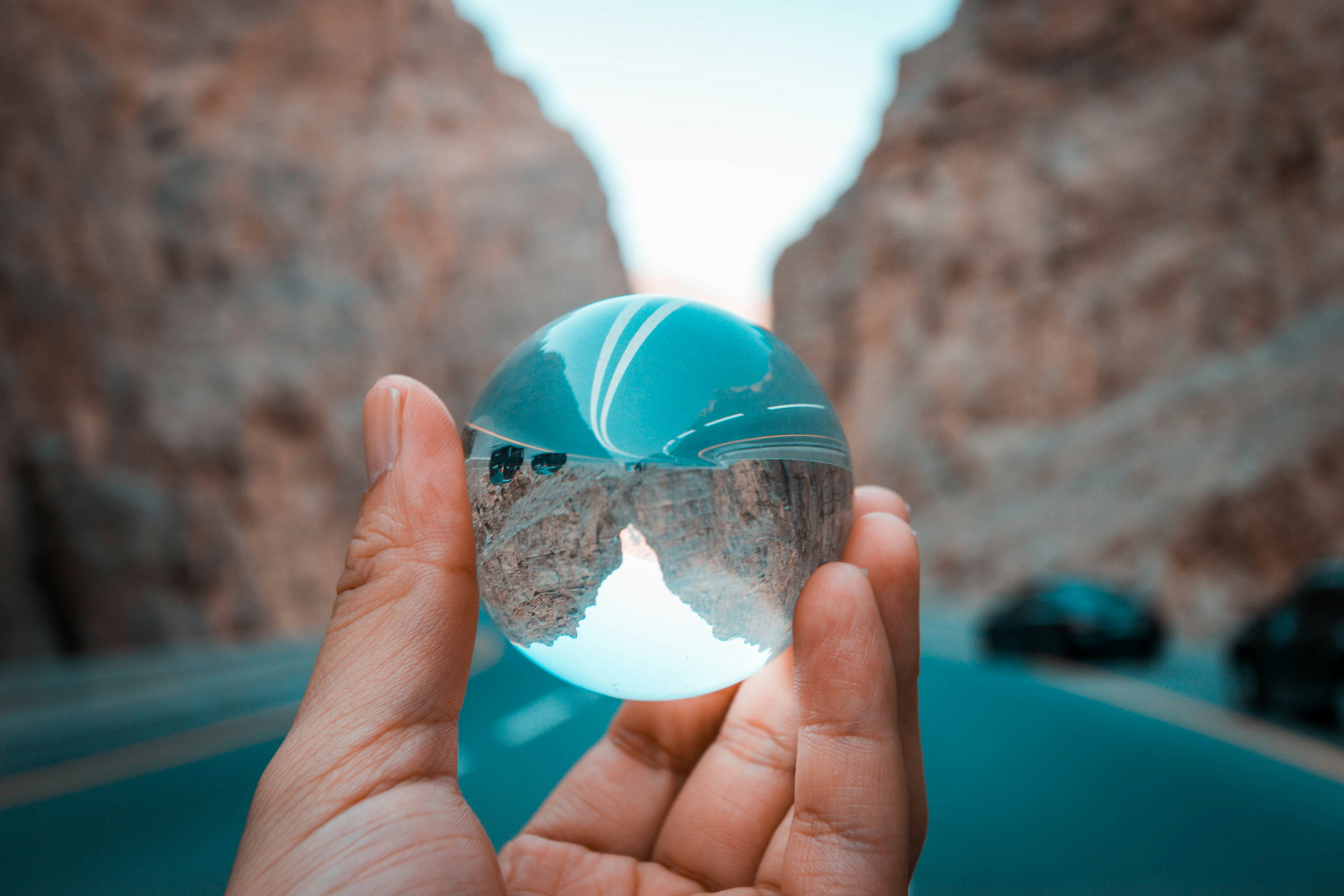 A hand holding a glass sphere that reflects a winding road flanked by towering rock formations. The scene captures the essence of adventure and exploration.