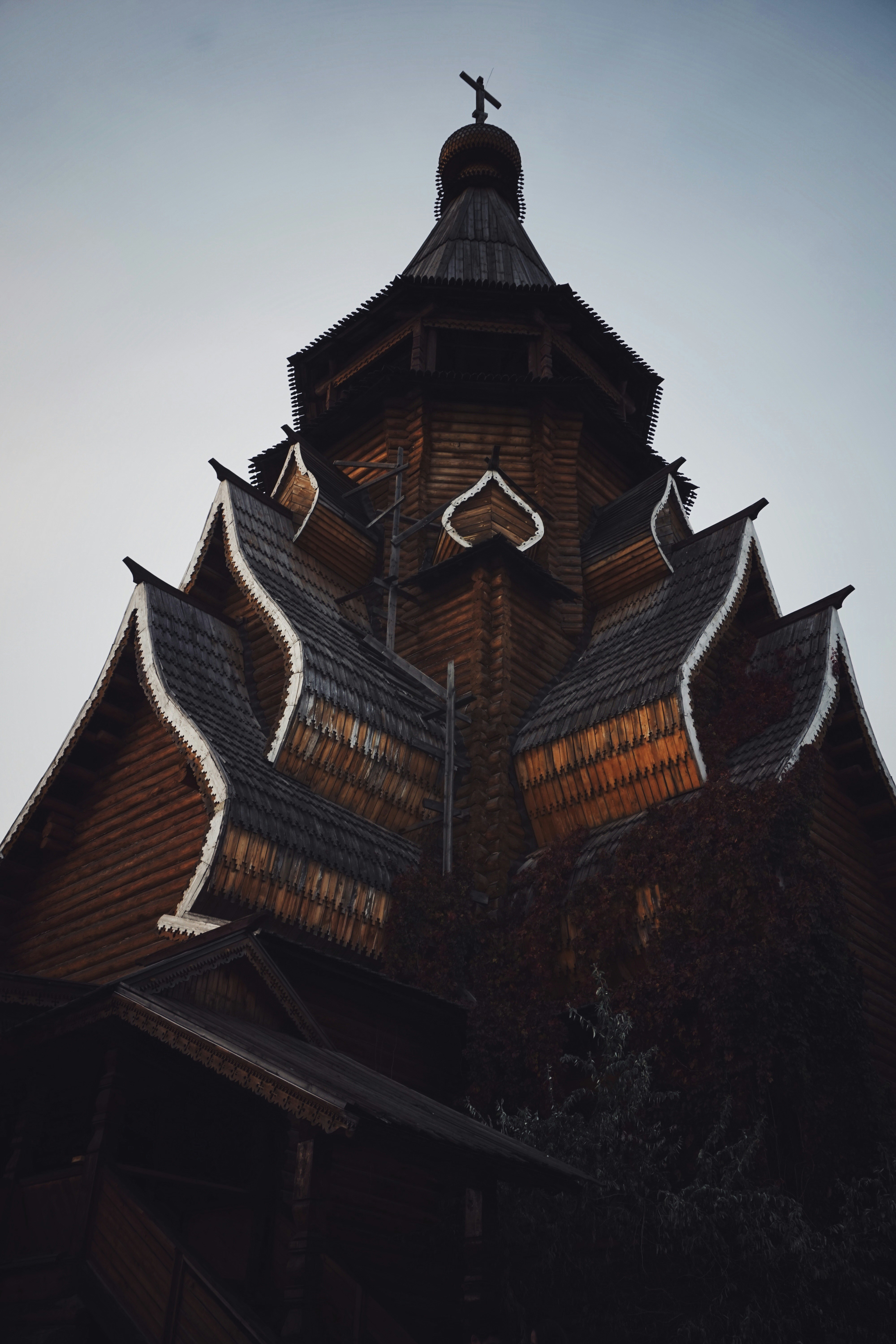 Intricate wooden architecture of a church tower reaching skyward, adorned with detailed carvings and a cross at the peak.