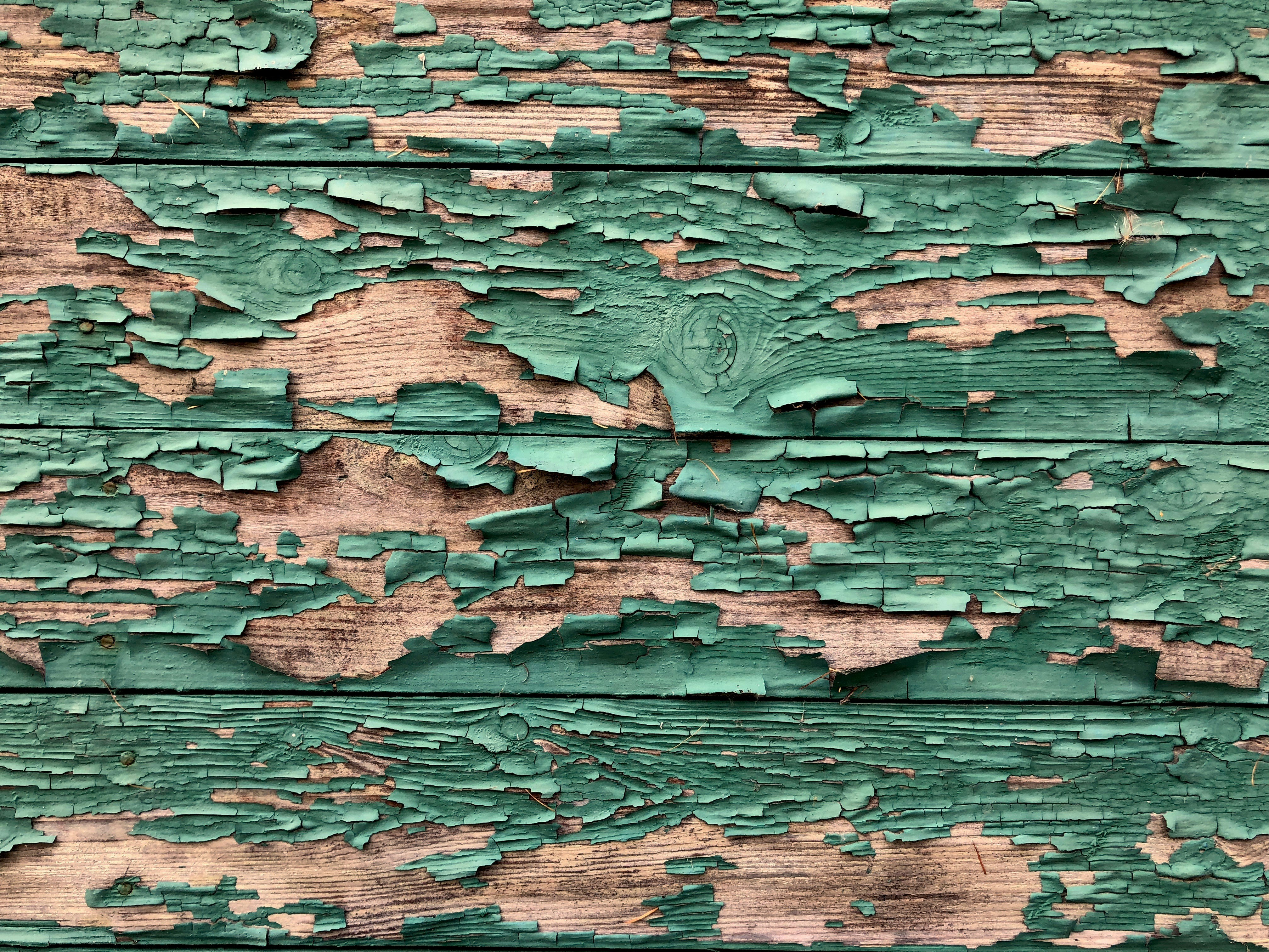 Close-up of peeling turquoise paint on wooden planks, revealing layers of history and texture.