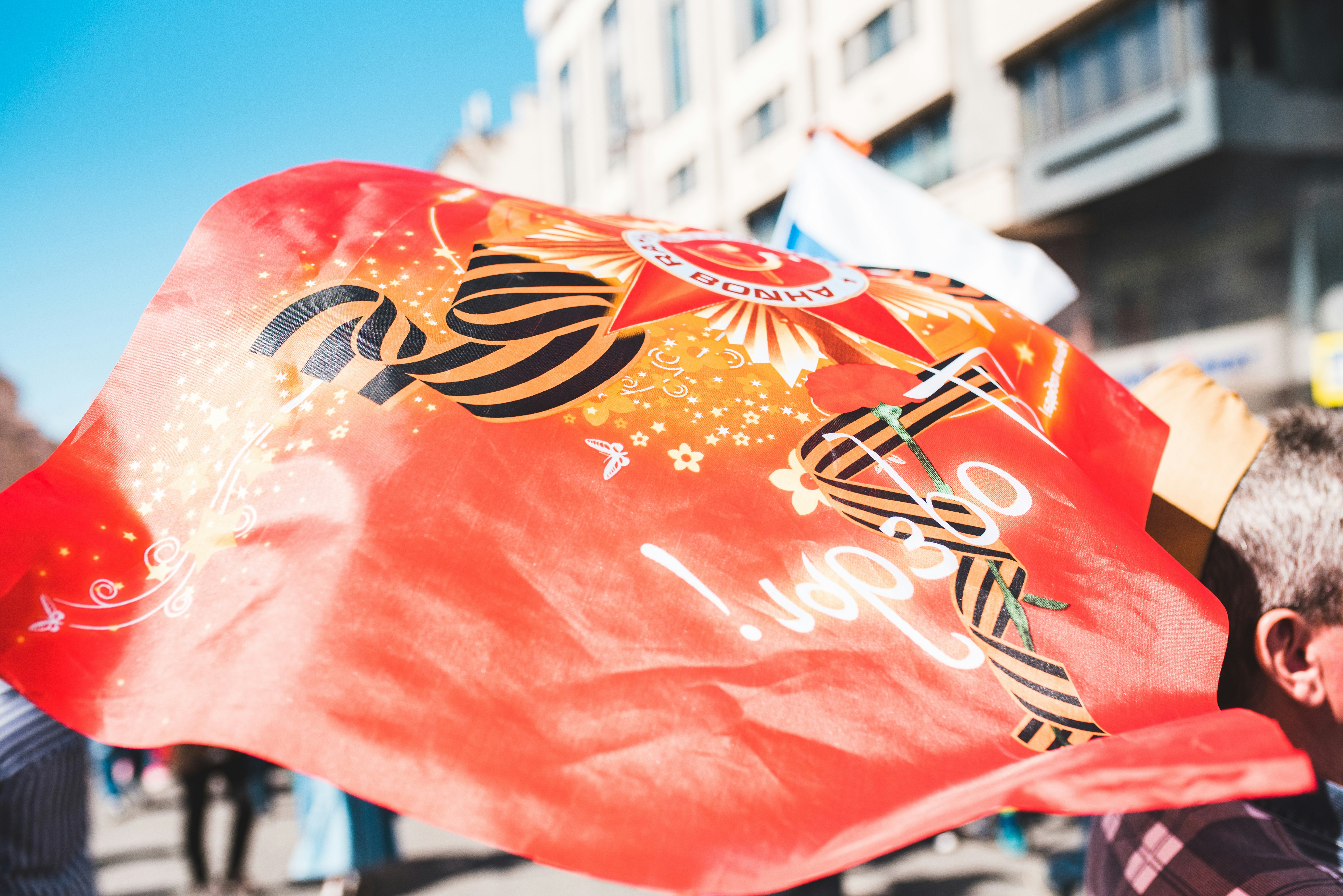 Crimson Banner in Motion: Ribboned Emblems Flutter Through a Sunlit Street