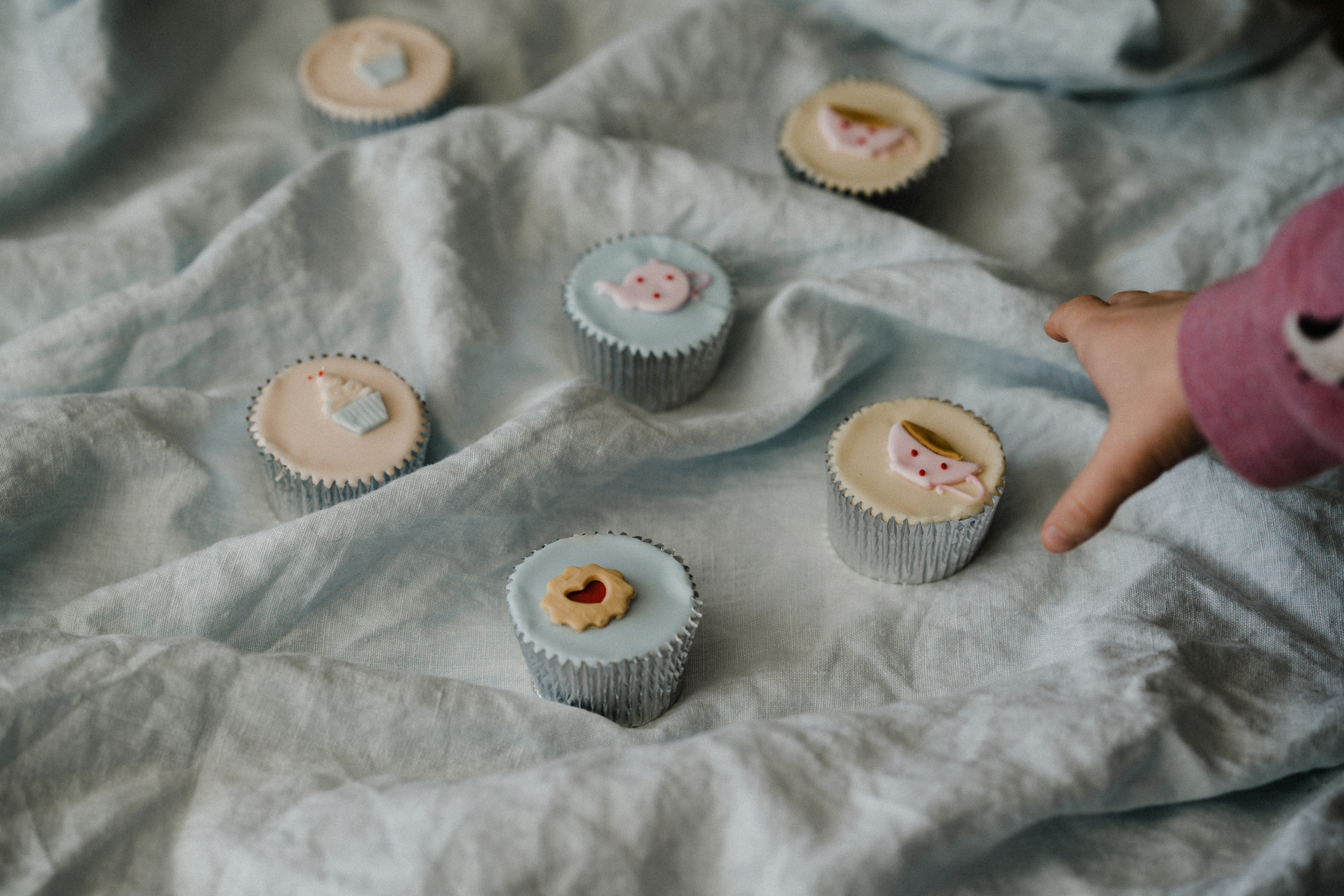 Blue-Topped Cupcake Amid Soft Linen: A Tiny Finger Guides the Gaze
