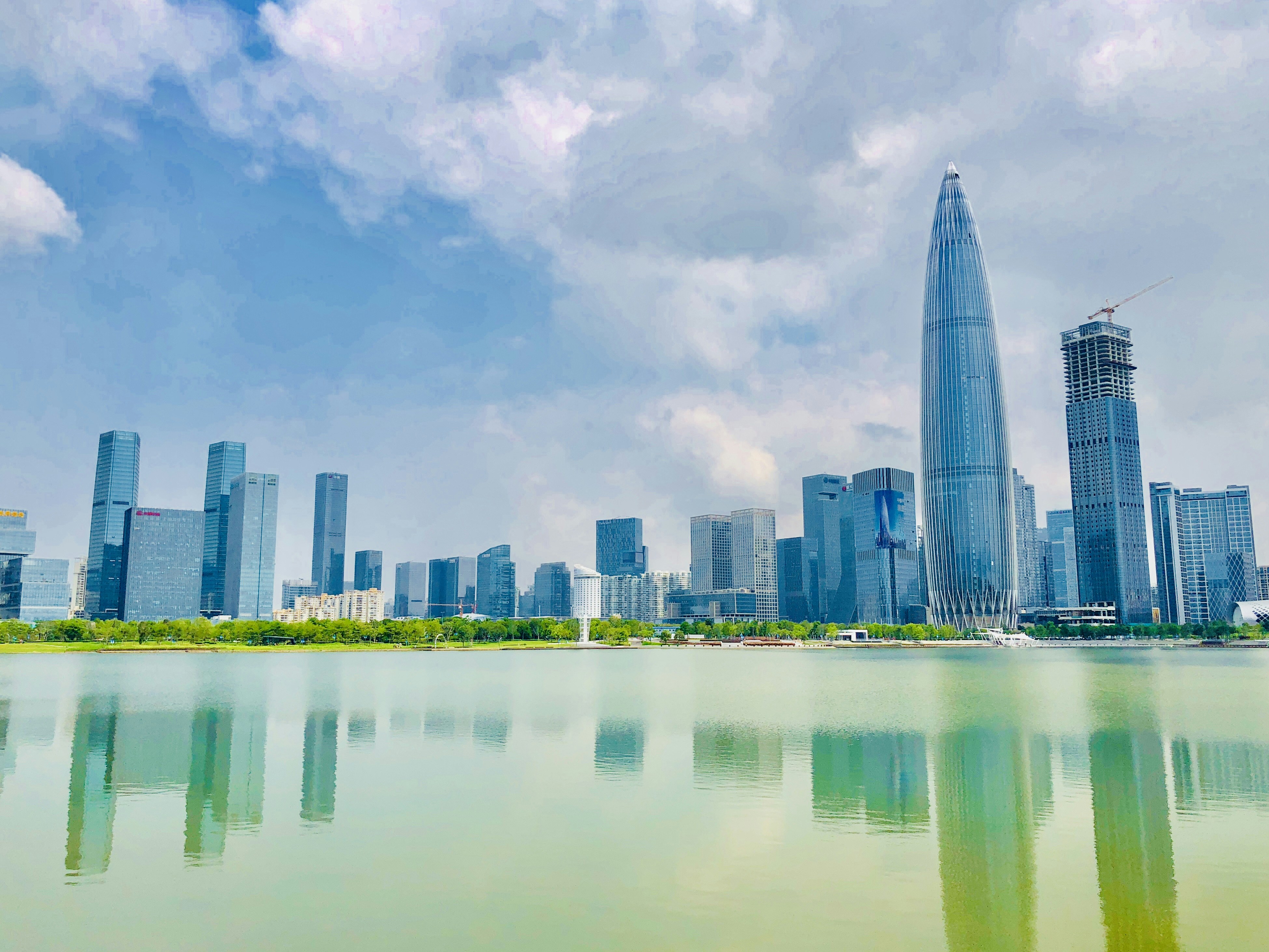 High-rise buildings reflecting in calm ocean waters under a partly cloudy sky.