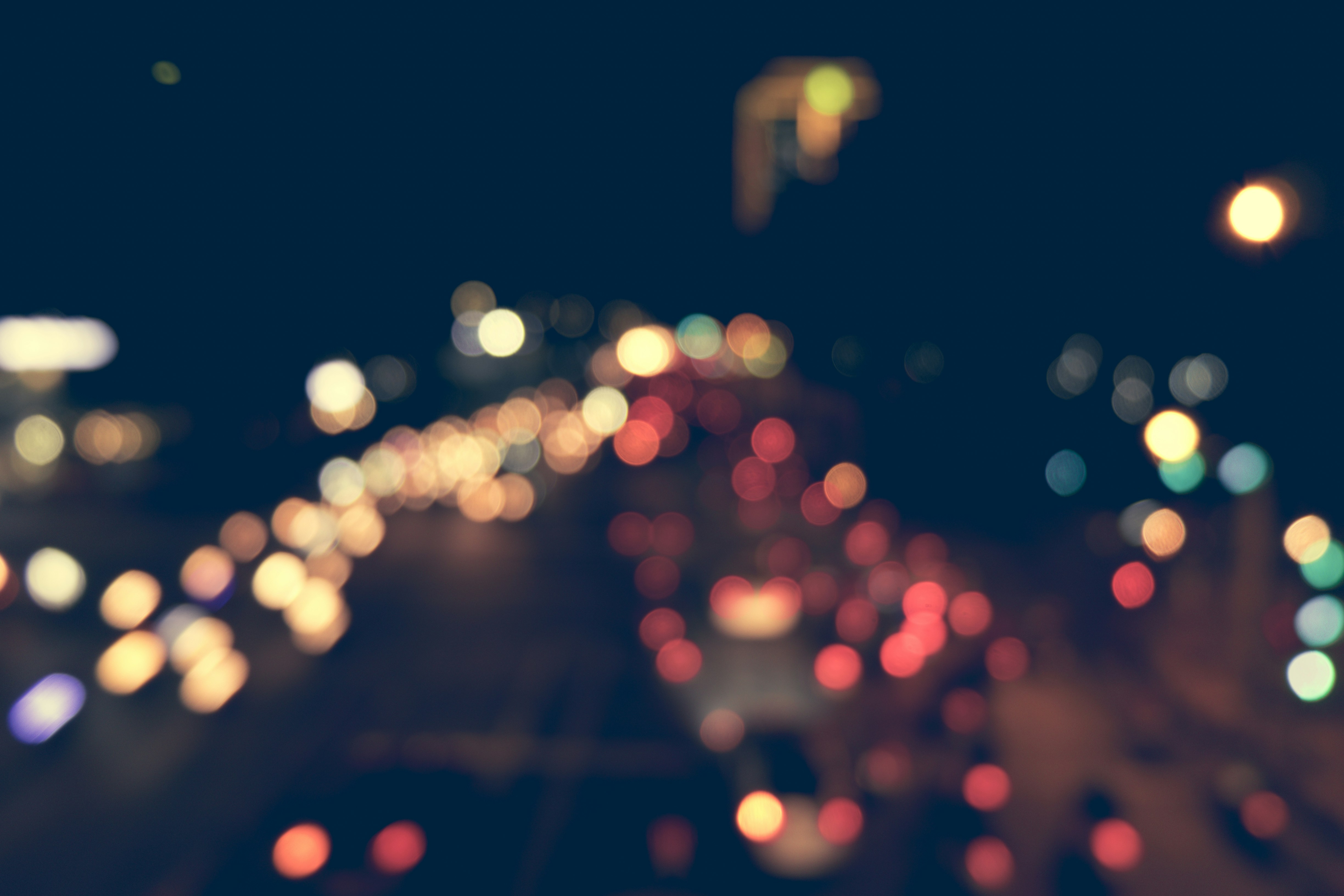 Night-city photograph rendered in soft bokeh with blurred headlights and streetlights along a busy roadway. The shallow depth of field emphasizes atmosphere and motion over sharp detail.