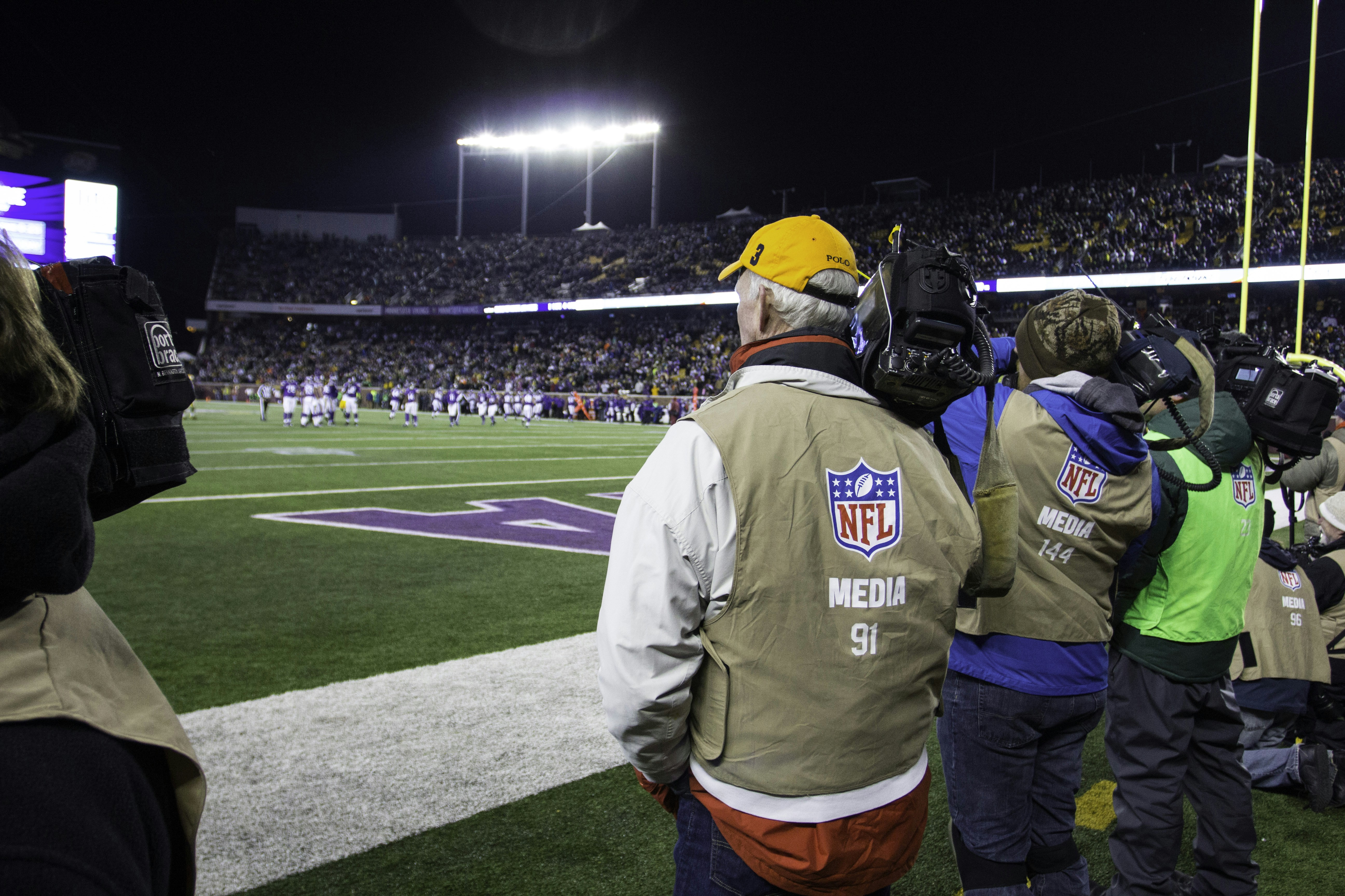 Sideline photographers capture an intense football game under bright stadium lights.