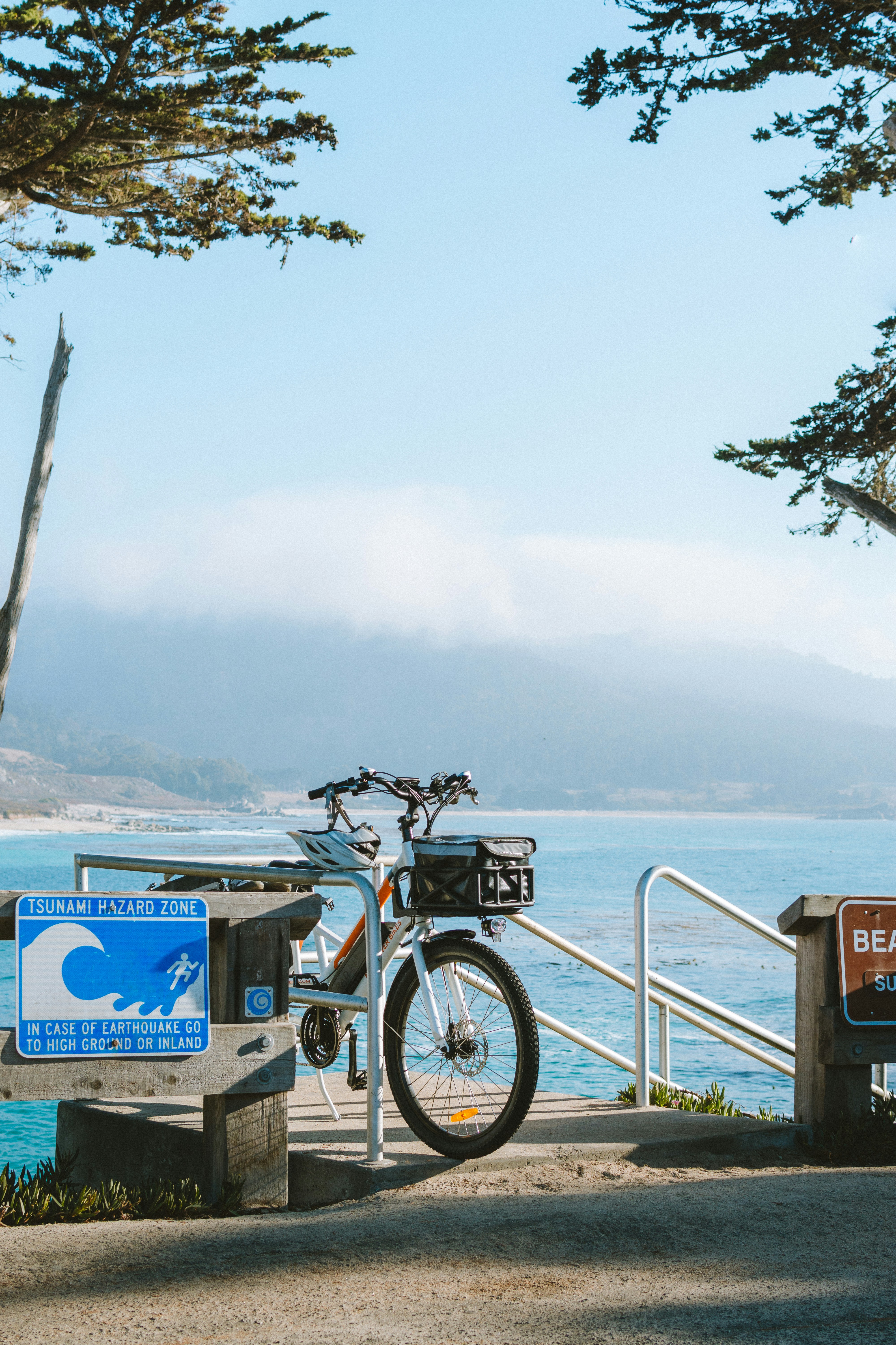 Bicycle parked on a wooden platform overlooking a serene coastal scene, flanked by warning signs about tsunami hazards. 
