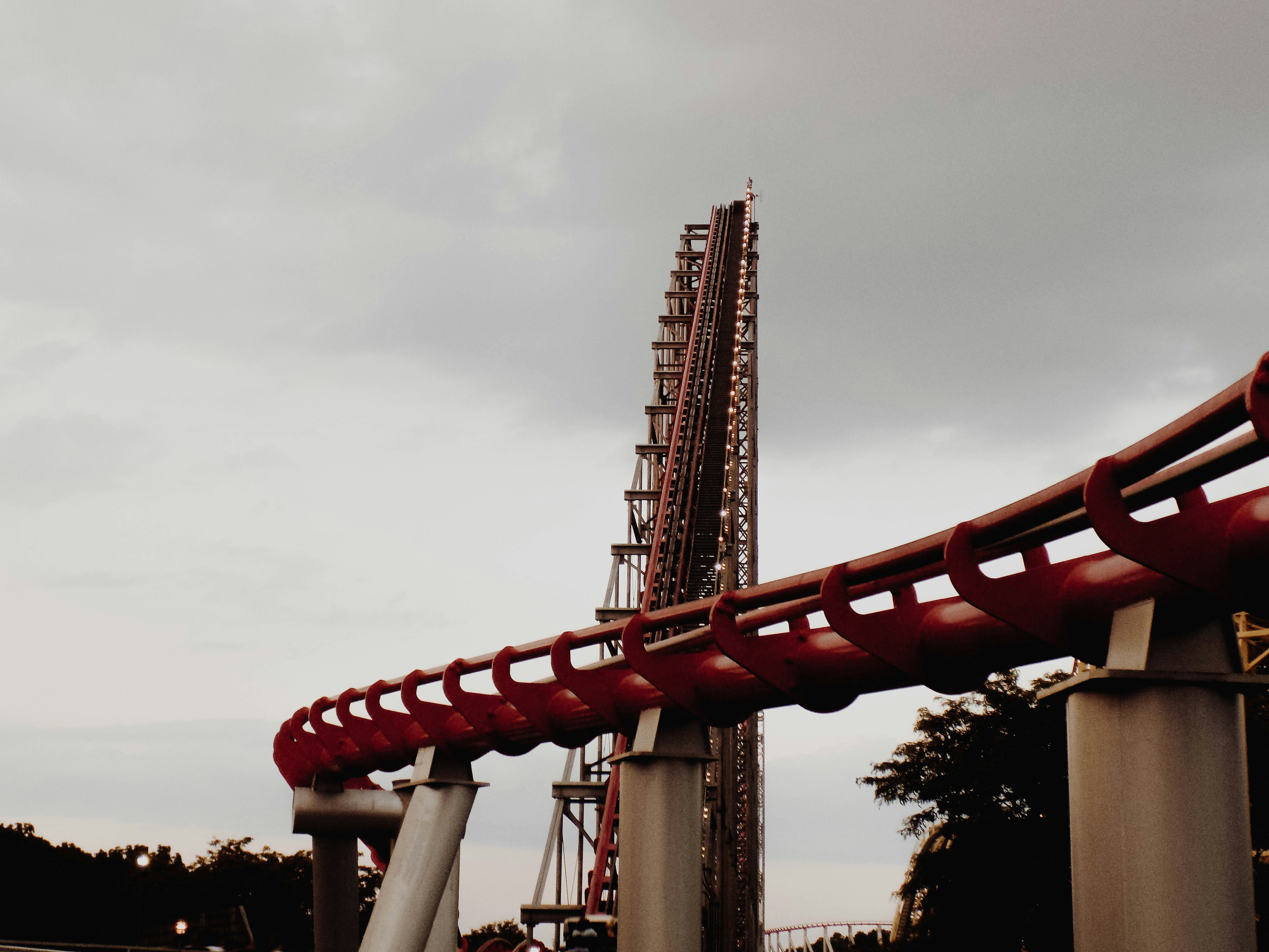 A roller coaster's red track curves dramatically against a cloudy sky, hinting at the thrill of the ride ahead. The towering ascent looms in the background.