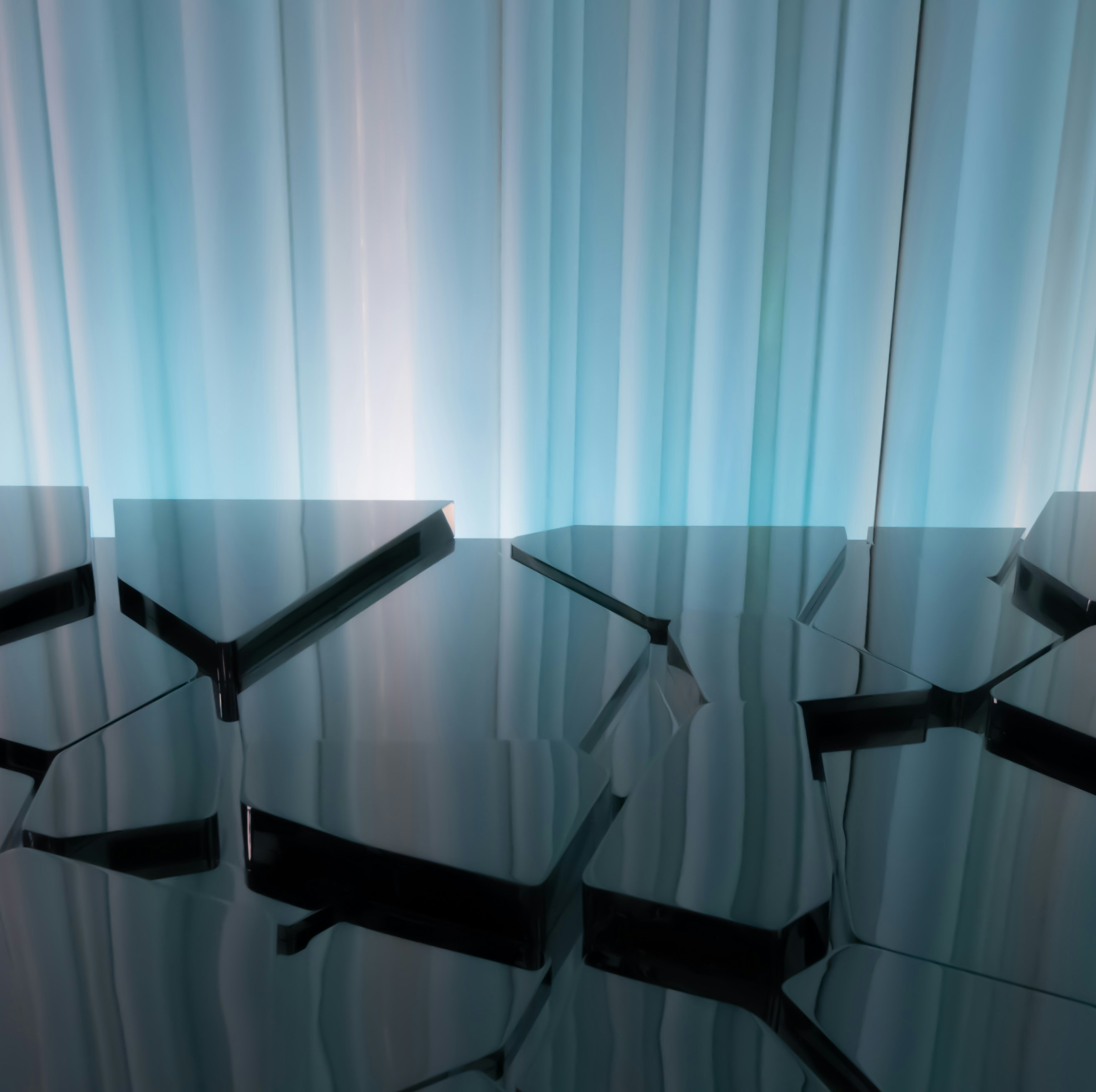Polished Monoliths Align on a Reflective Surface Beneath a Cyan Curtain