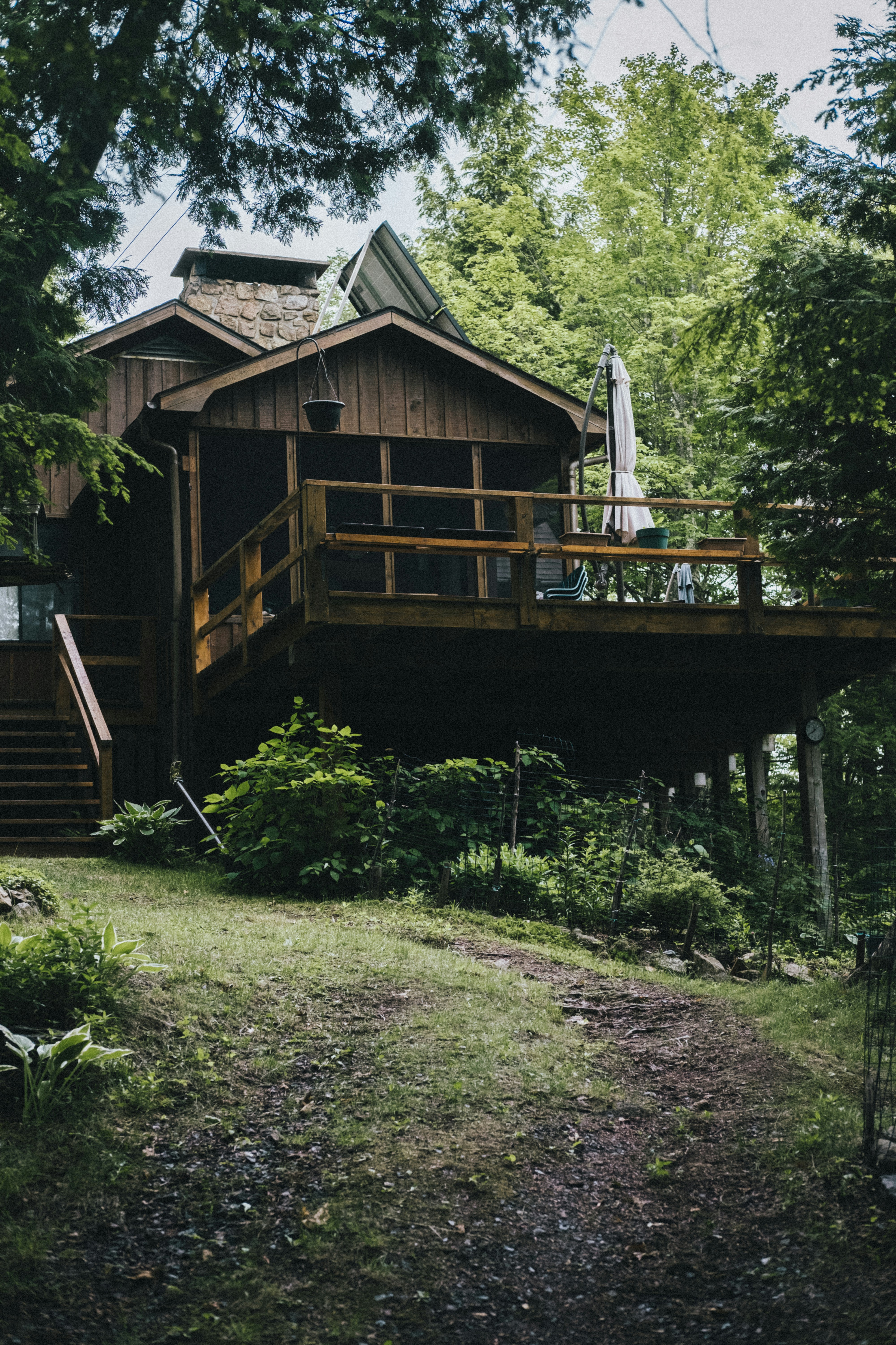 A charming wooden cabin nestled among lush greenery, featuring a spacious deck and inviting steps leading to the entrance.