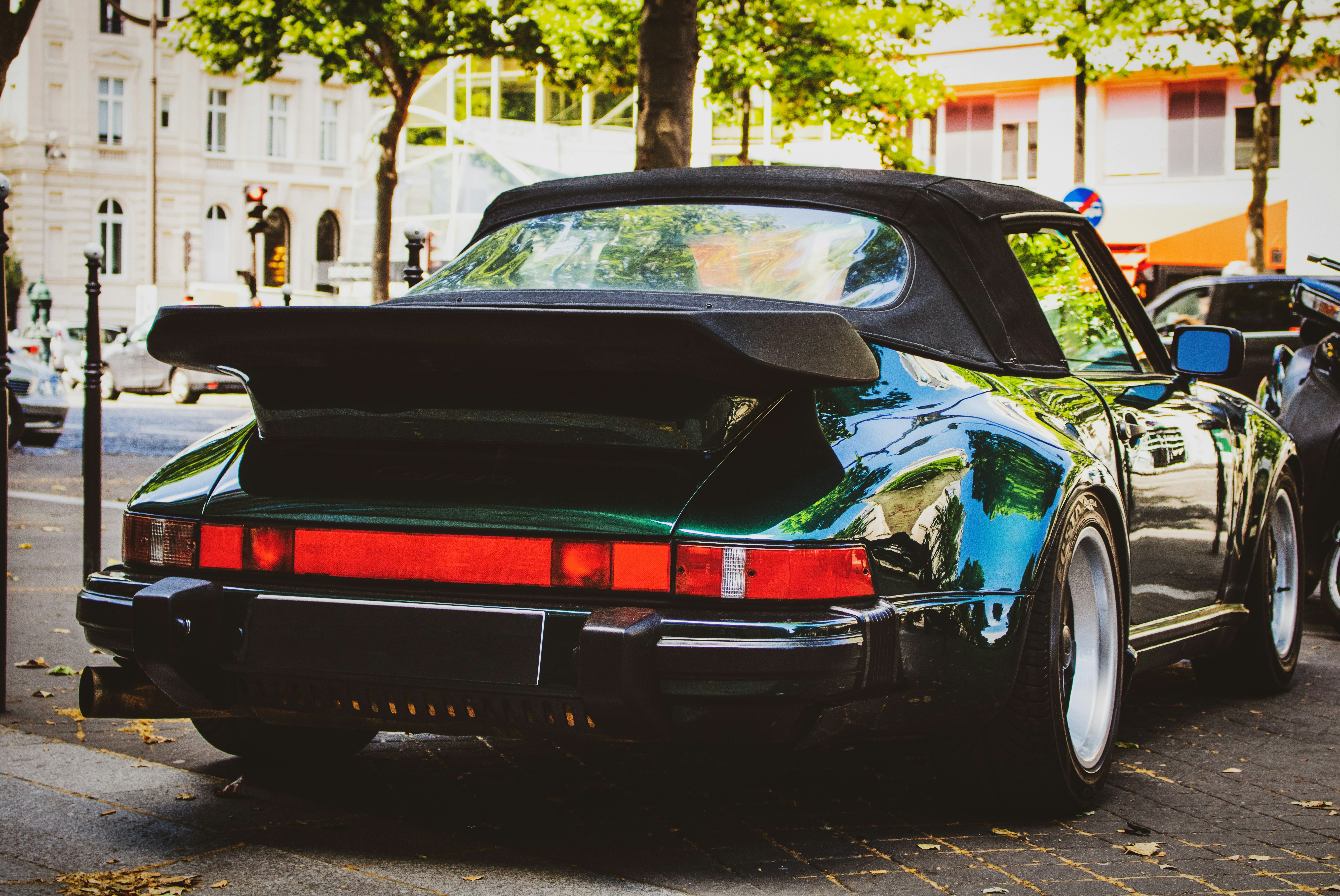 Rear-View Gleam: A dark-green vintage convertible resting on a sunlit city street
