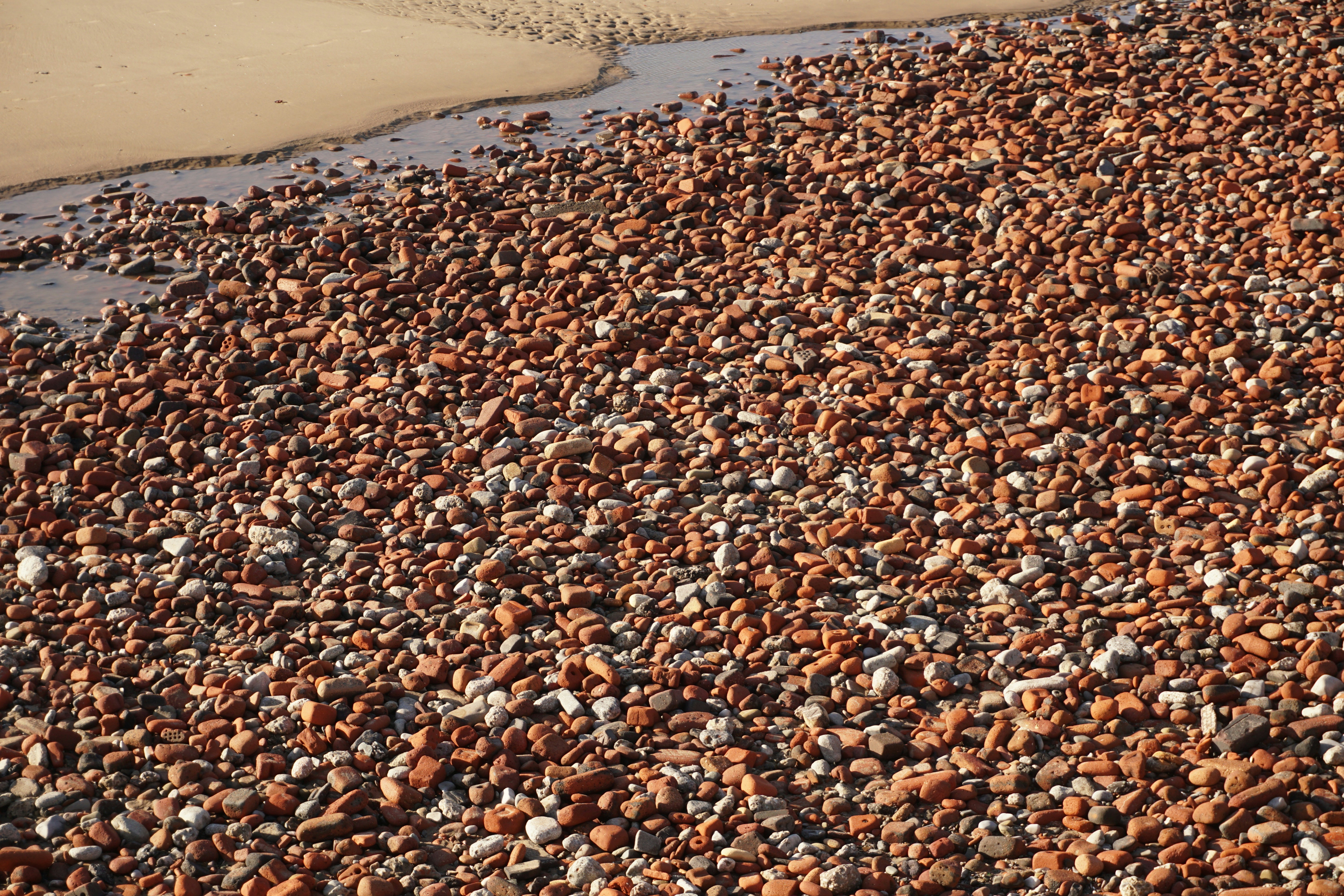 This unique shot features a beach covered in brick rubble originating from historic Liverpool buildings. The unusual texture and warm tones of the bricks against the neutral sand create a visually interesting background, perfect for adding depth to designs or marketing materials.
