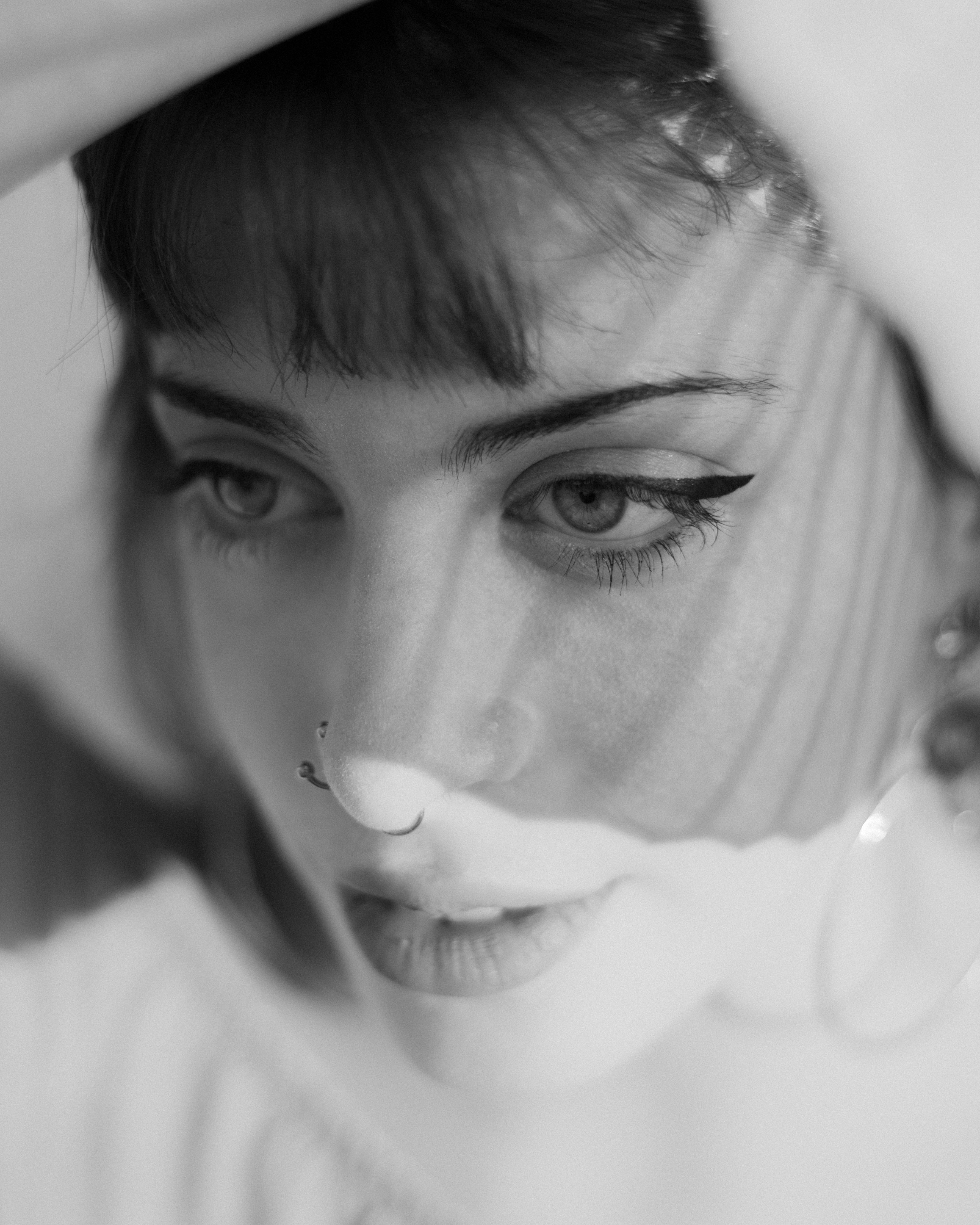 Close-up portrait showcasing a young woman with striking features, highlighted by soft shadows and a delicate play of light across her face.