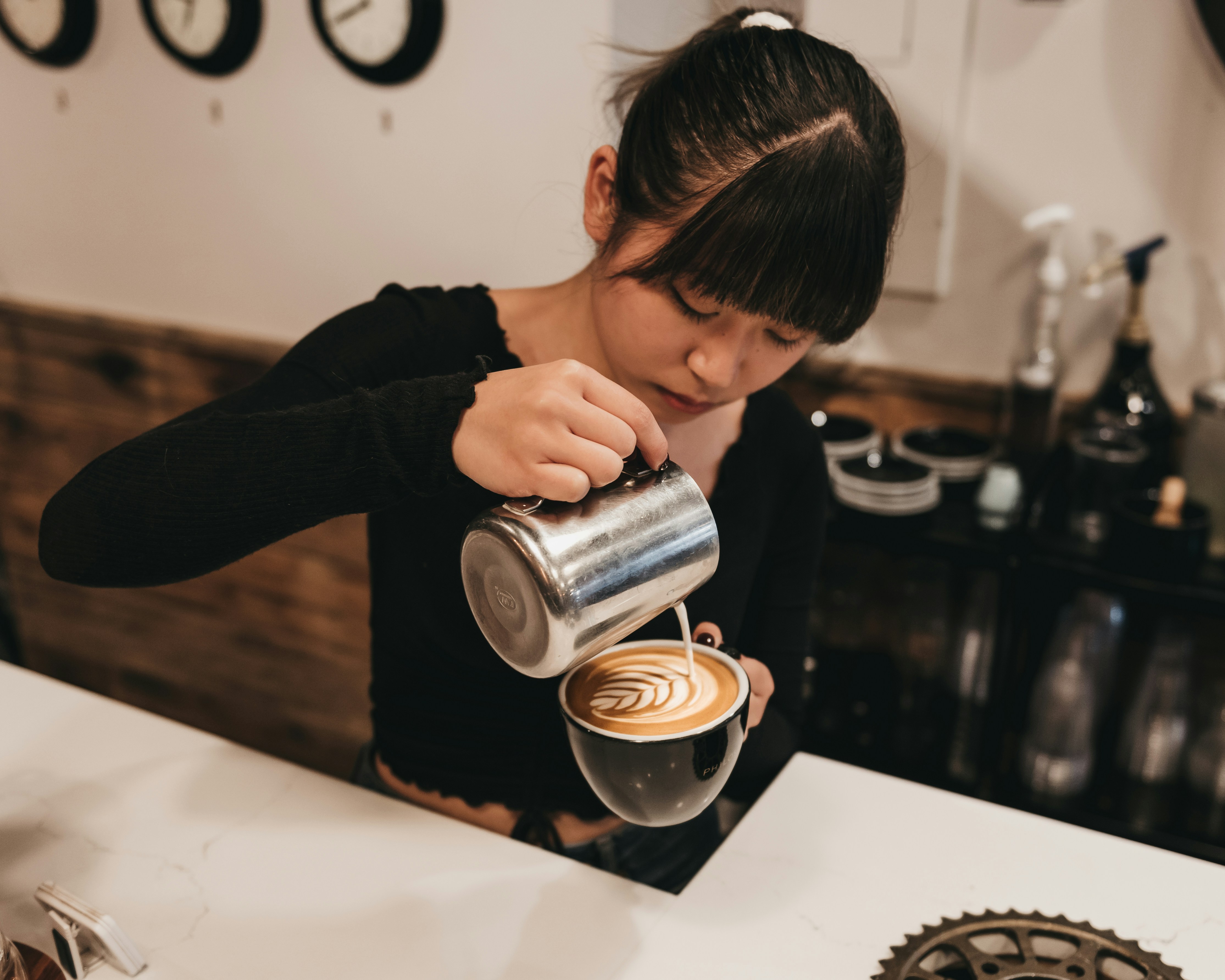 Barista skillfully pouring milk into a coffee cup at a café counter.