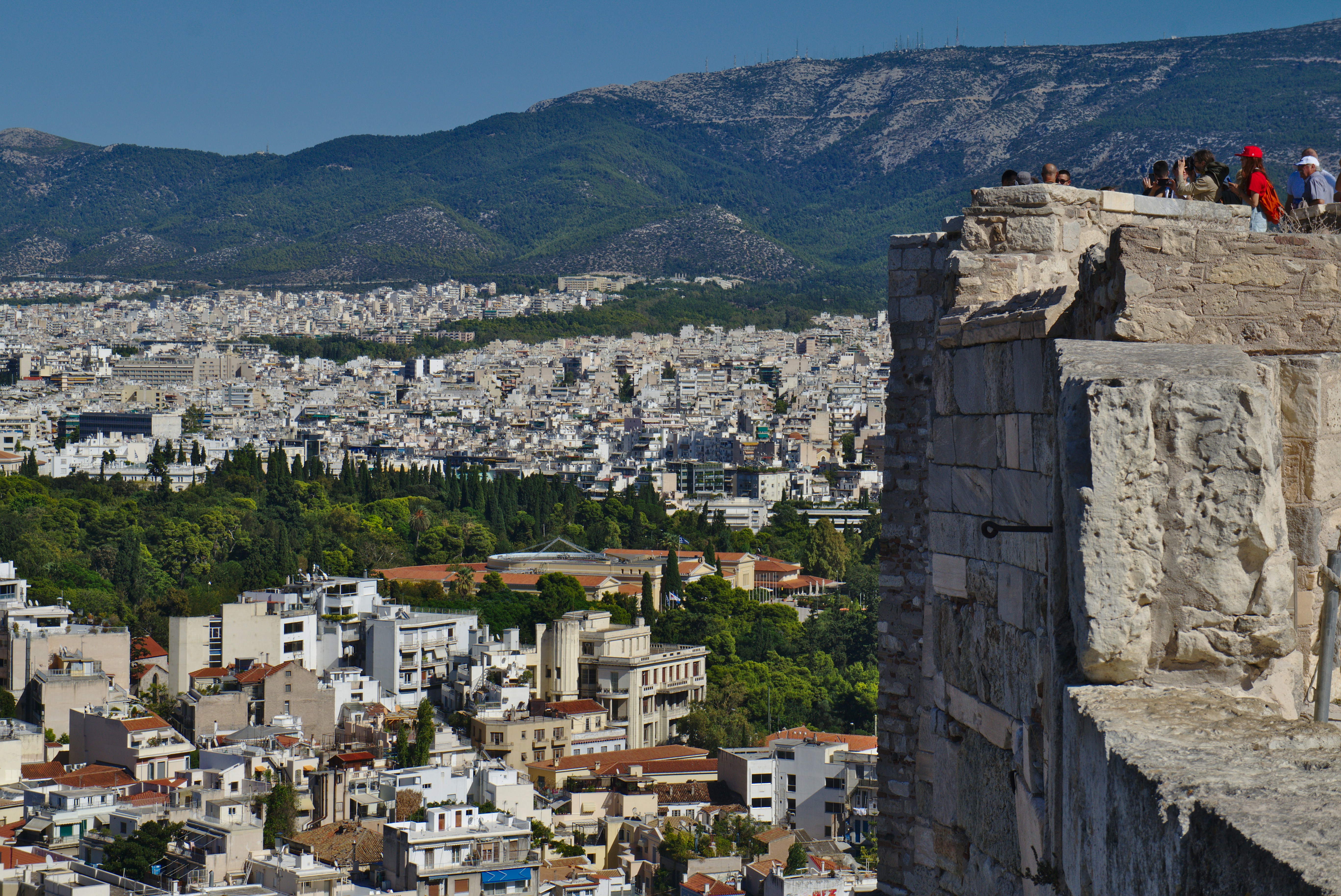 View from a stone fortress overlooking a sprawling city against a backdrop of lush green hills.