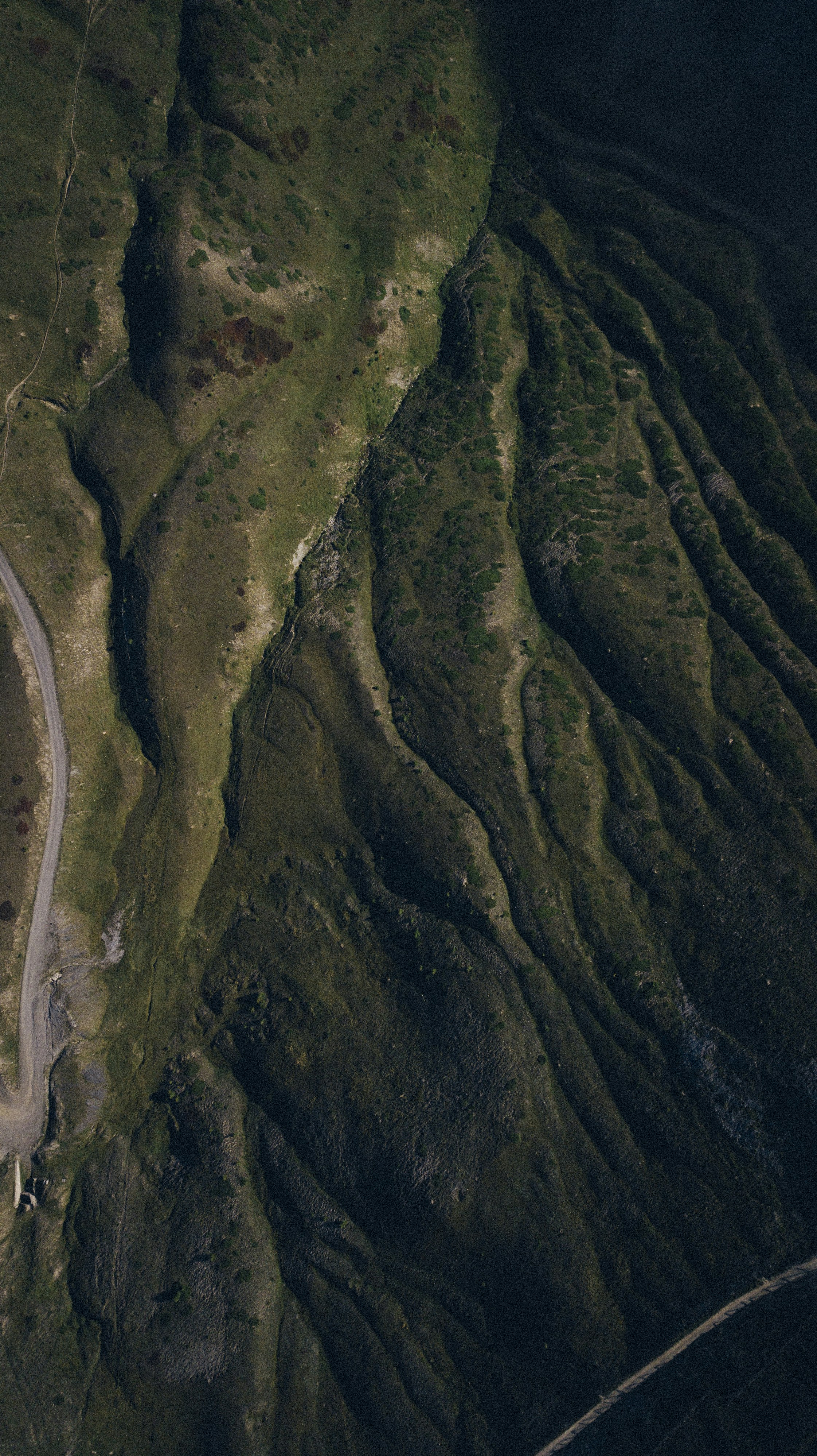 Aerial view showcasing the intricate patterns of the landscape, with winding paths and textured greenery. The interplay of light and shadow highlights the natural contours of the terrain.