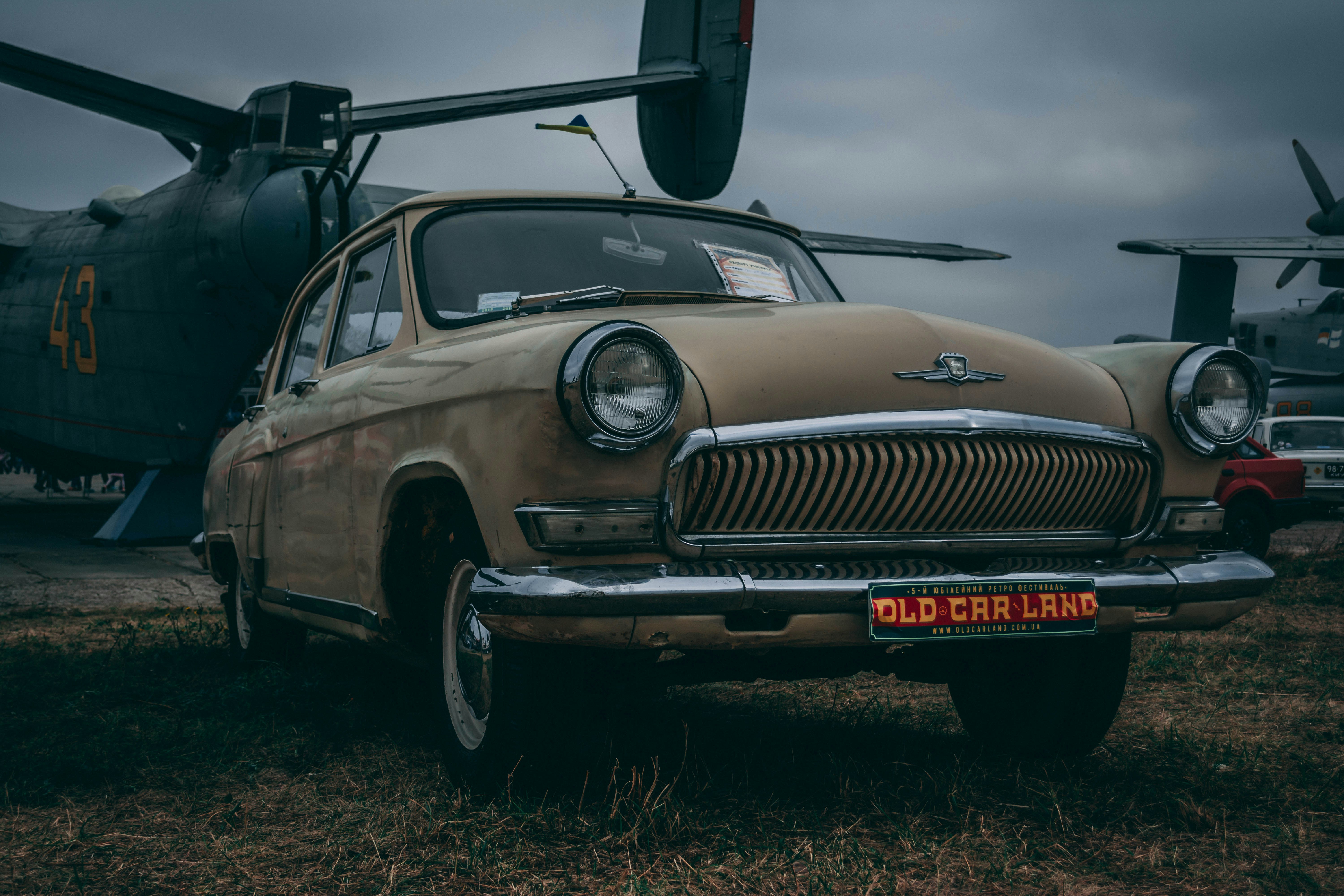 Classic car parked in front of an old aircraft on a cloudy day.