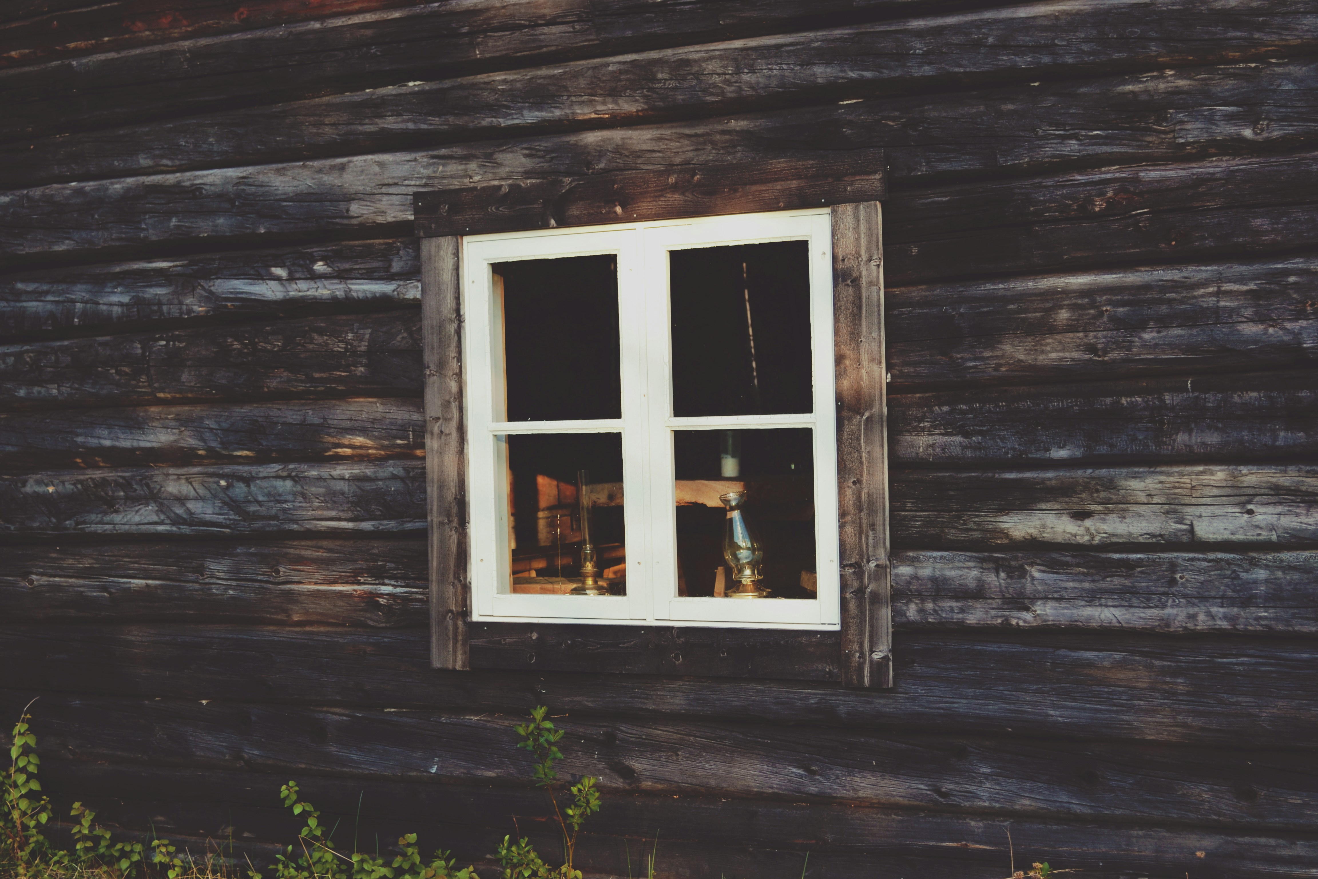 A rustic window framed in weathered wood, revealing a glimpse of the interior with soft lighting. The surrounding logs enhance the nostalgic atmosphere.