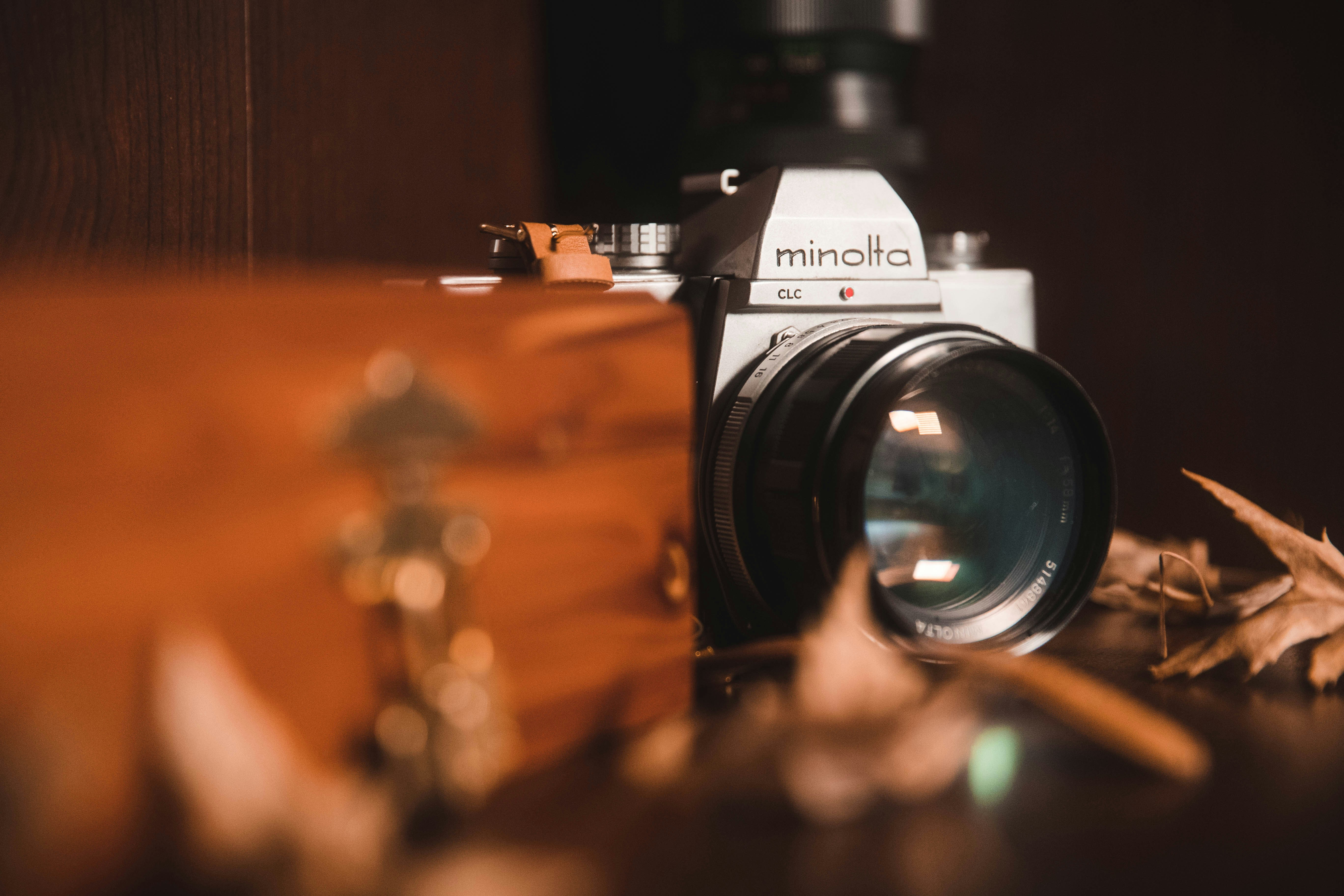 Classic Minolta camera resting on a wooden surface surrounded by autumn leaves, highlighting vintage photography aesthetics.