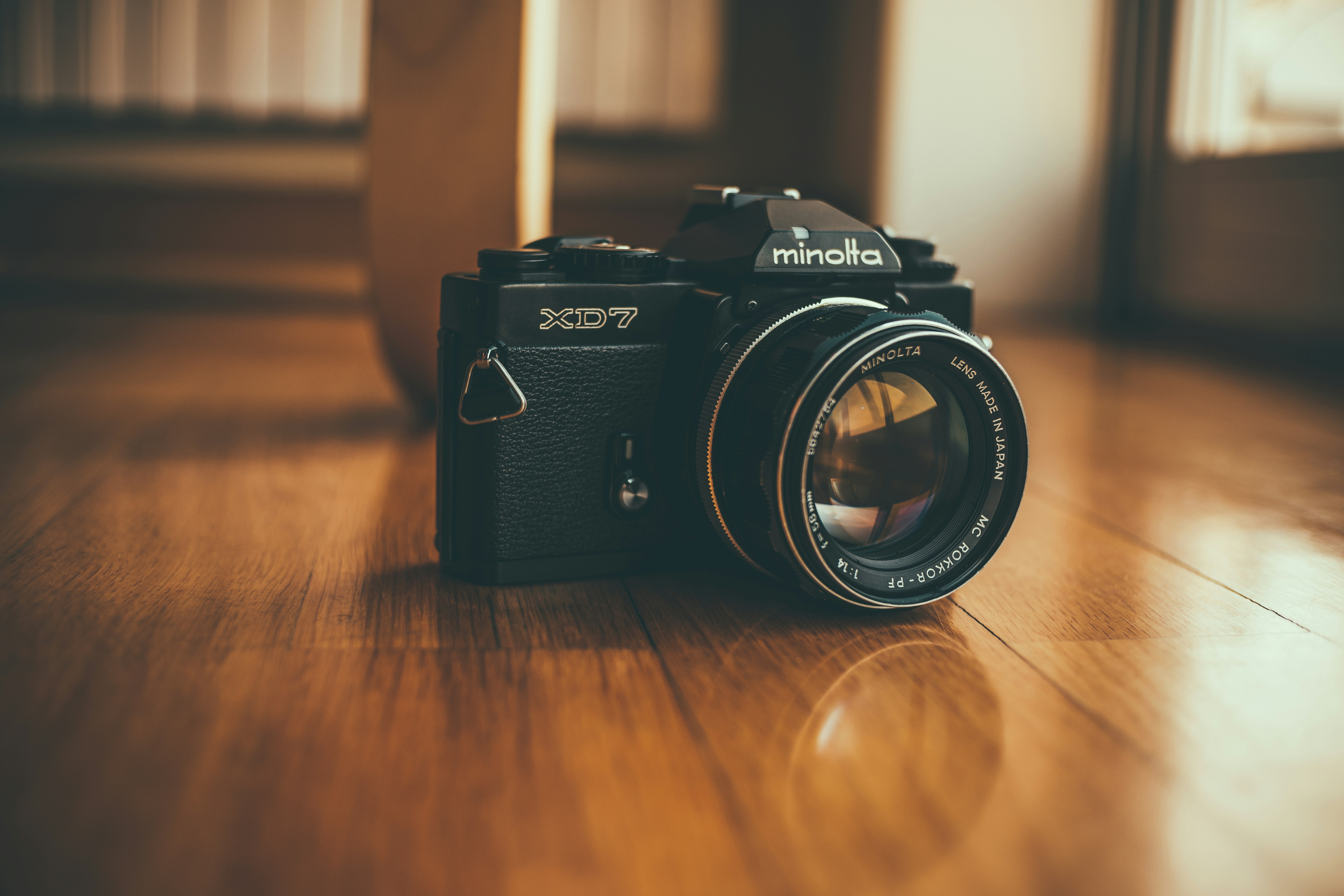 Minolta XD7 camera resting on a polished wooden floor with soft lighting.