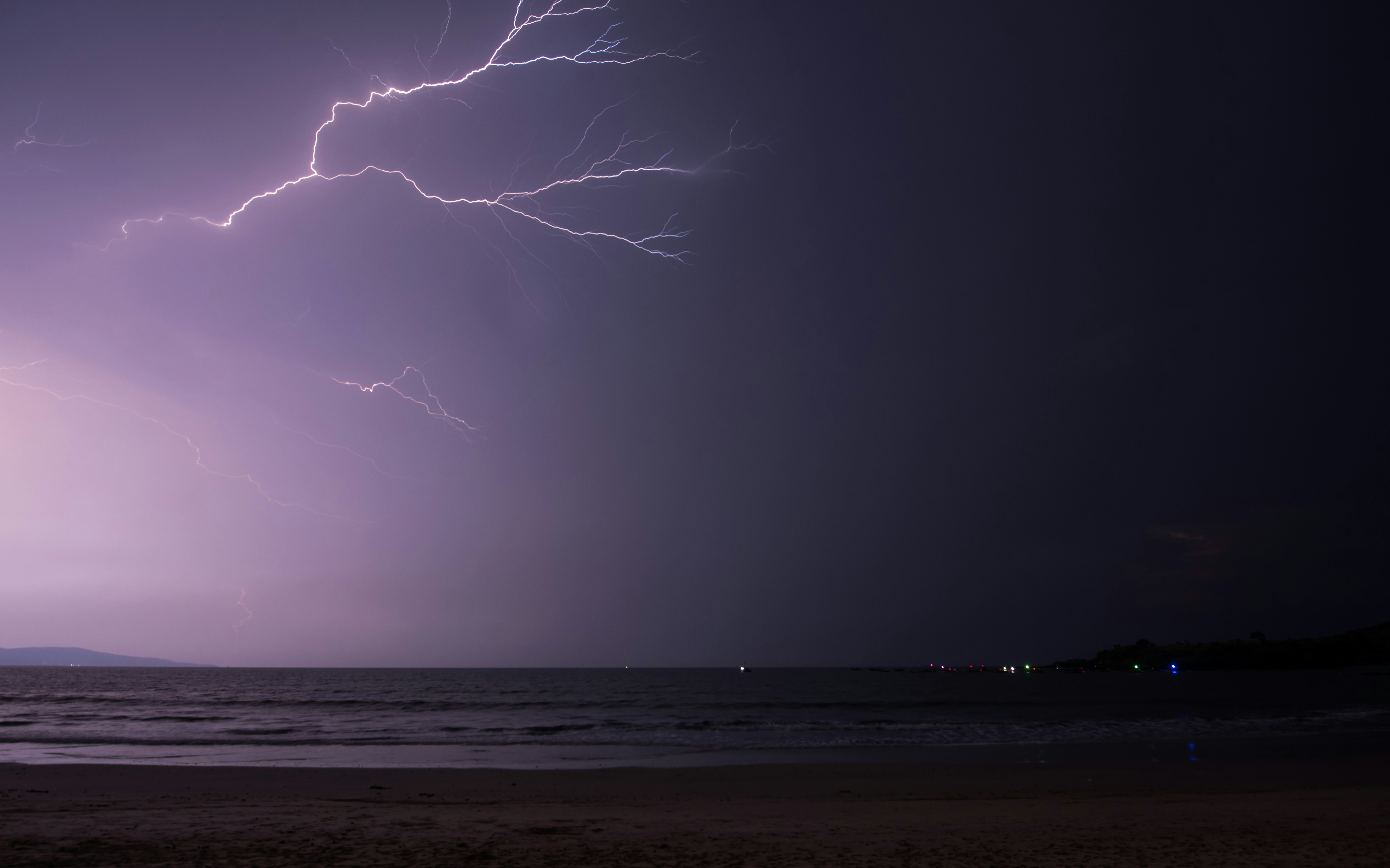 Lightning forks illuminating the dark sky over a tranquil beach at night.