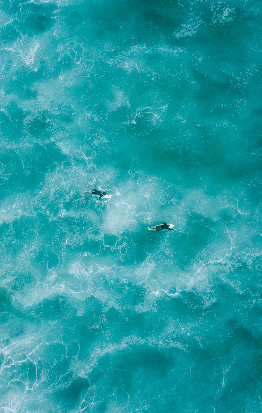 Two surfers navigating the turquoise waters, surrounded by frothy waves under a bright sky.