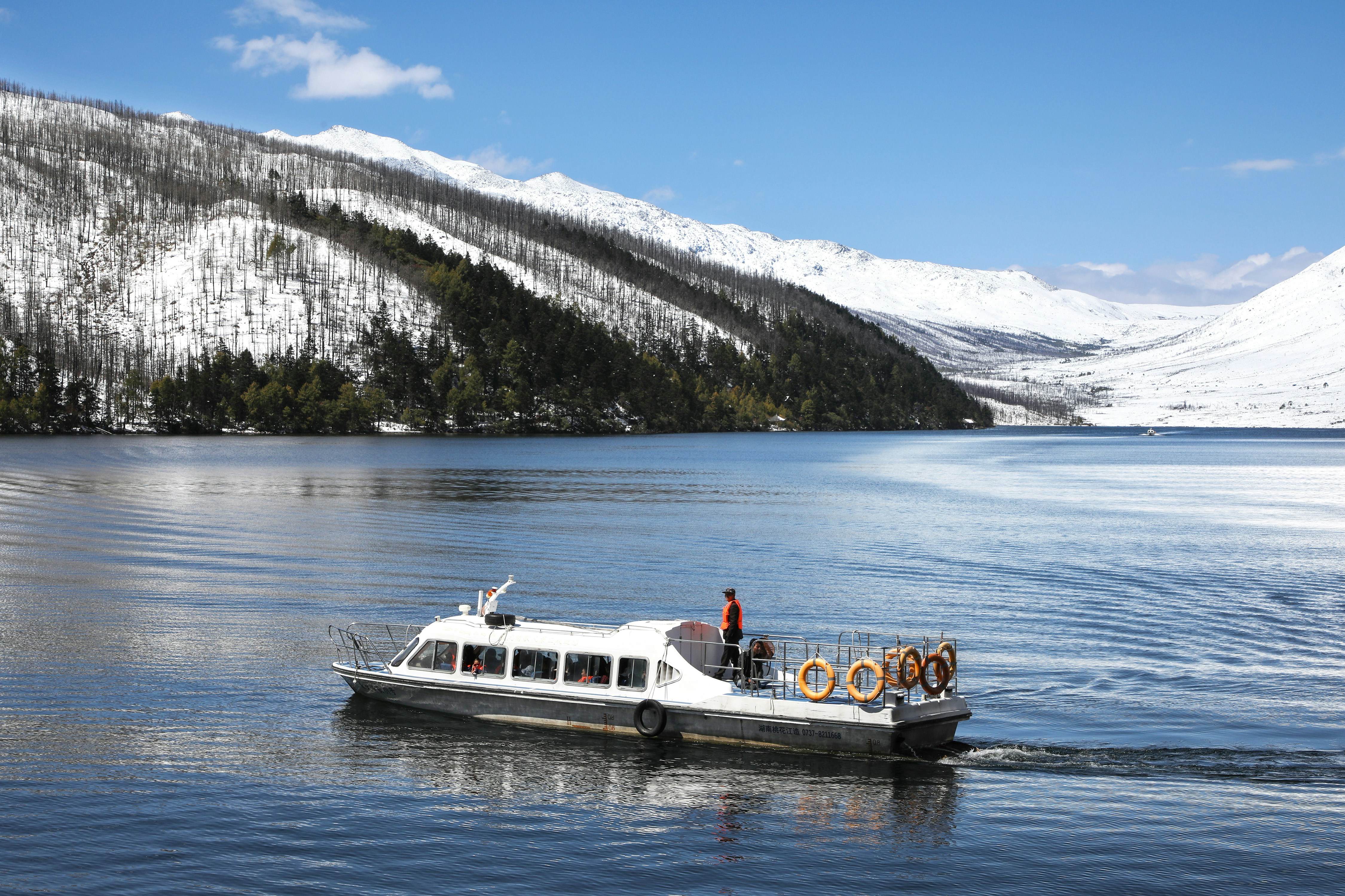 Boat gliding on a serene lake with snow-covered mountains in the background under a clear blue sky.