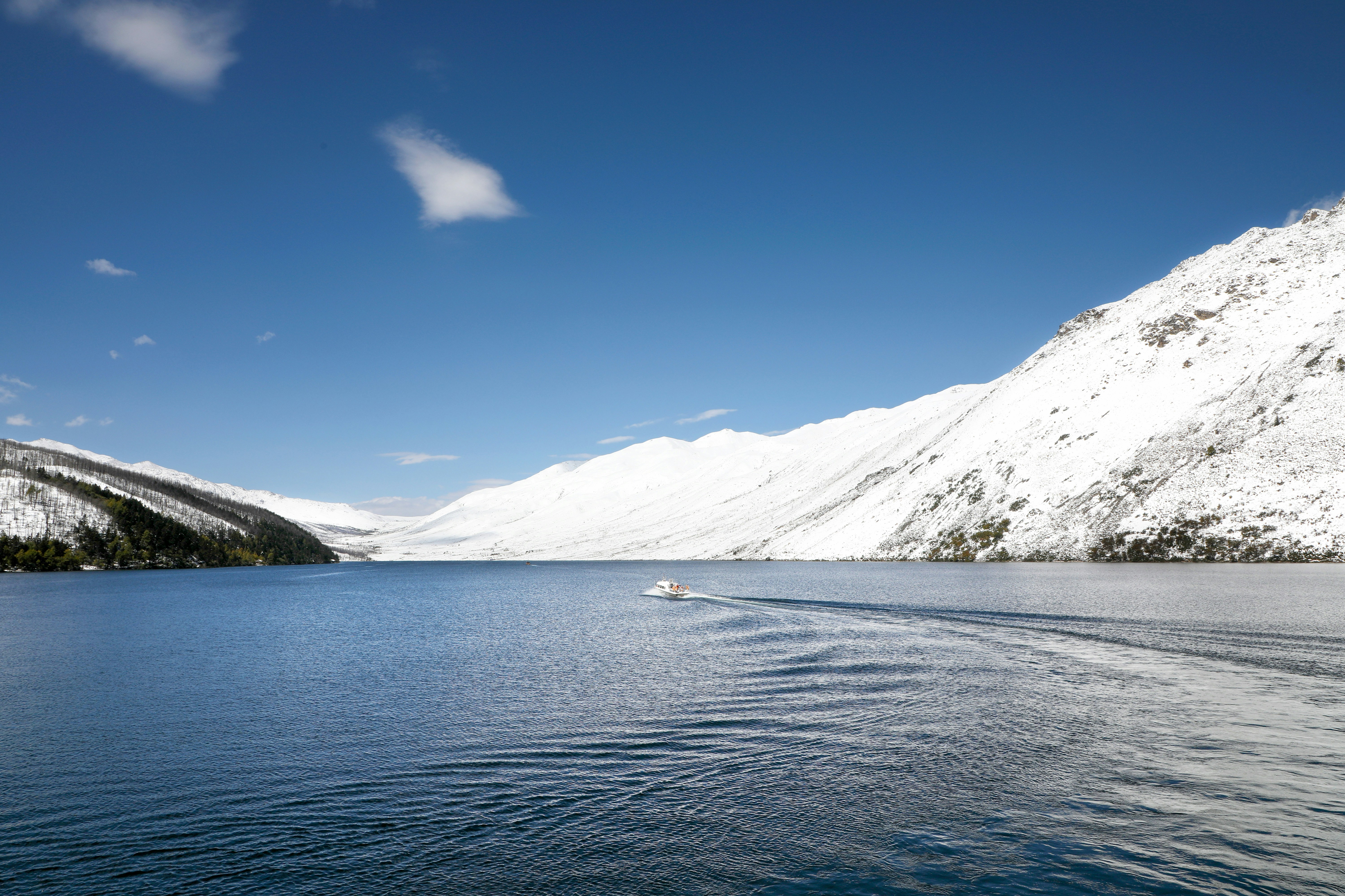 Lone Boat Tracing a Cerulean Wake Beneath Snow-Dusted Alpine Peaks