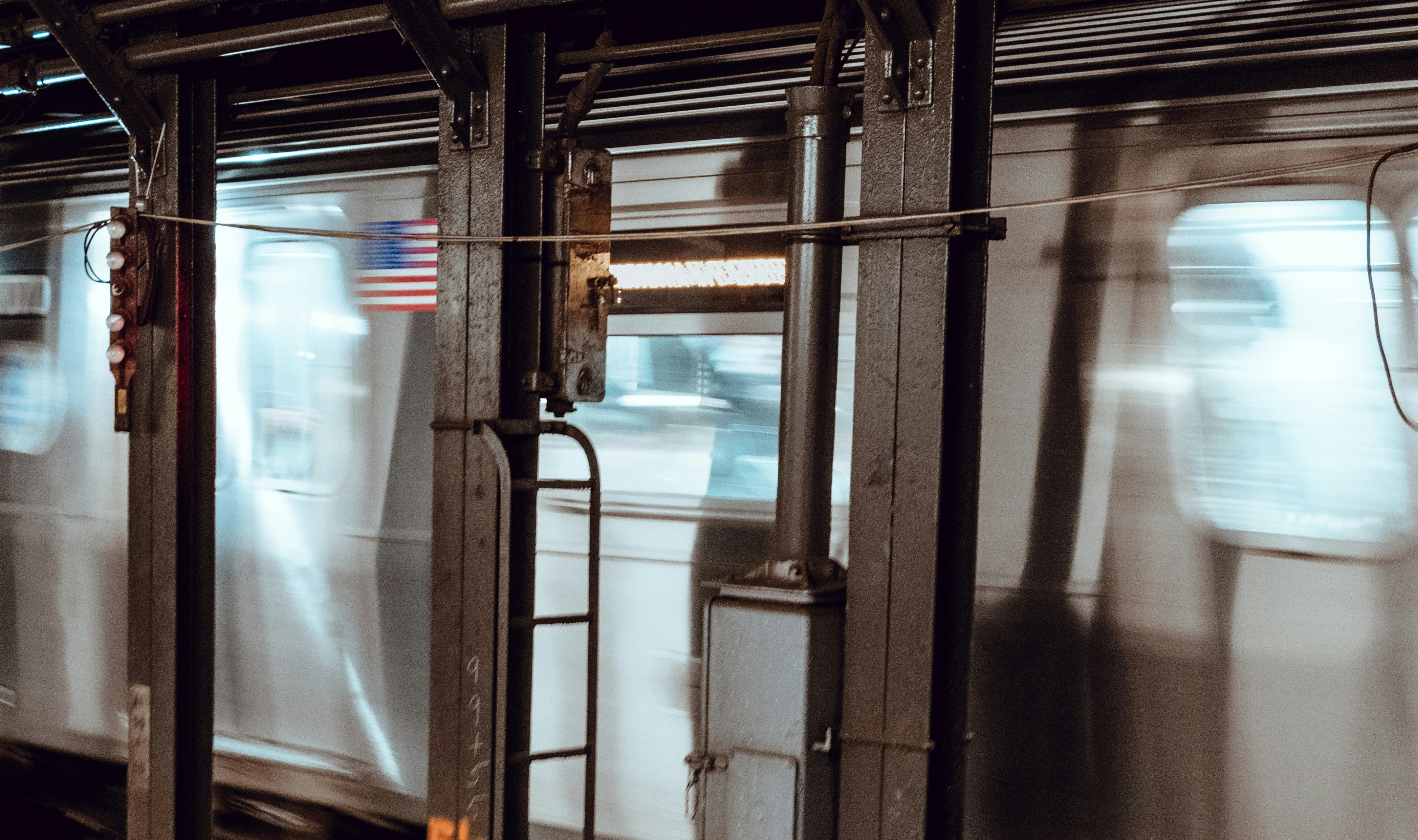 A subway train blurs past a station, emphasizing the speed of urban transit. The American flag adds a touch of patriotism to the industrial scene.