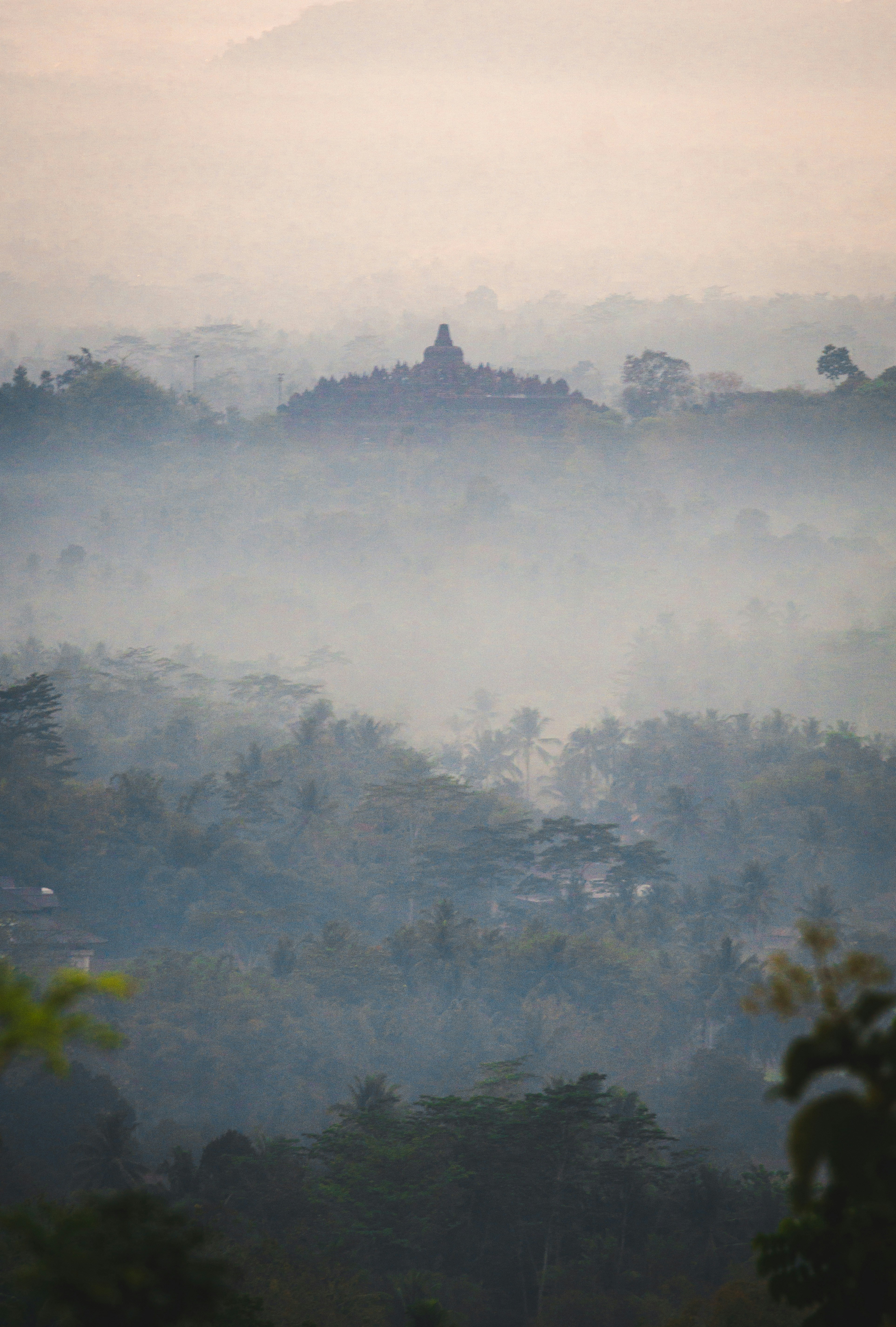 Misty landscape revealing the silhouette of a historical temple amidst lush greenery at dawn.