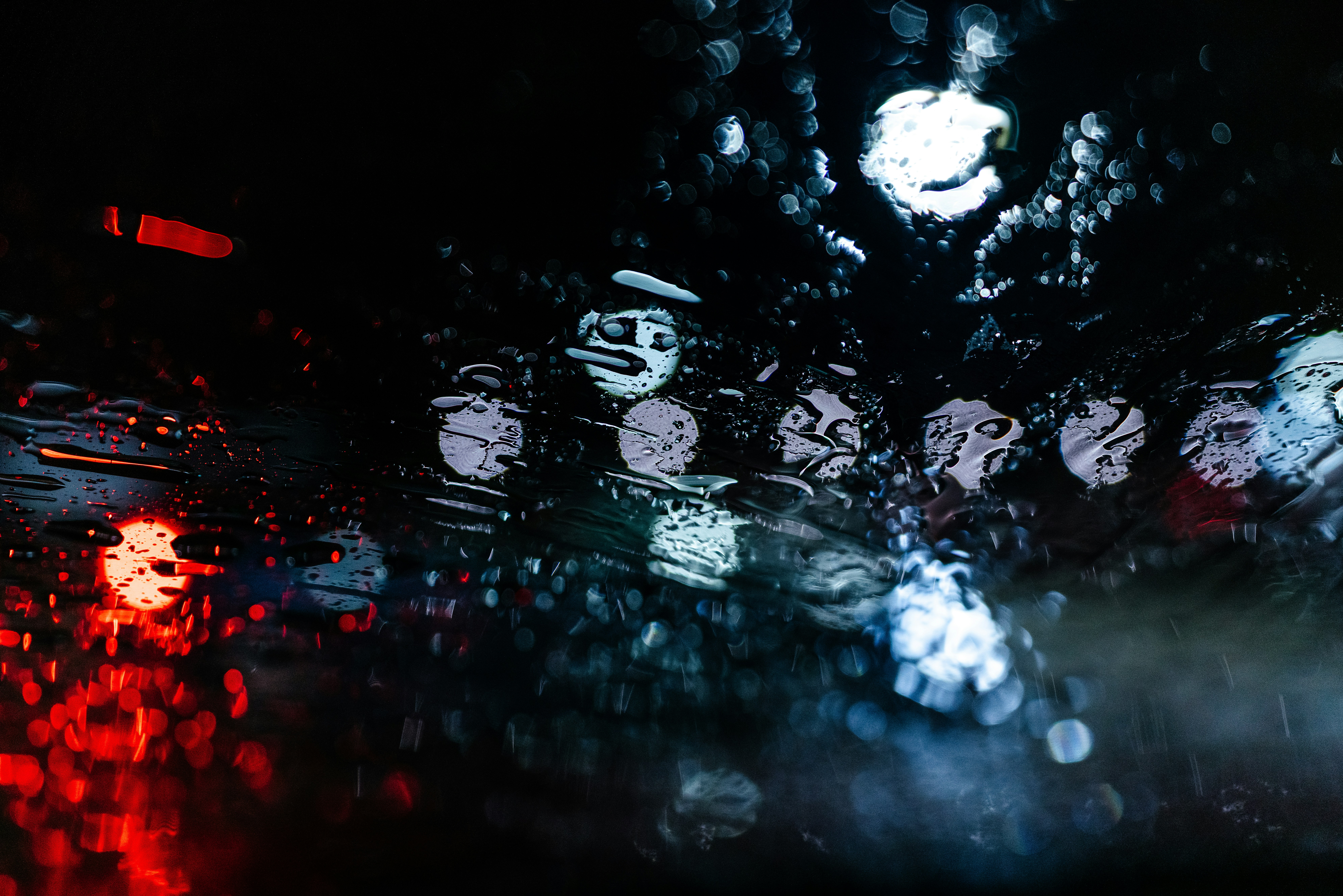 Abstract reflections of colorful lights distorted by raindrops on glass. The interplay of light and water creates a mesmerizing visual experience.
