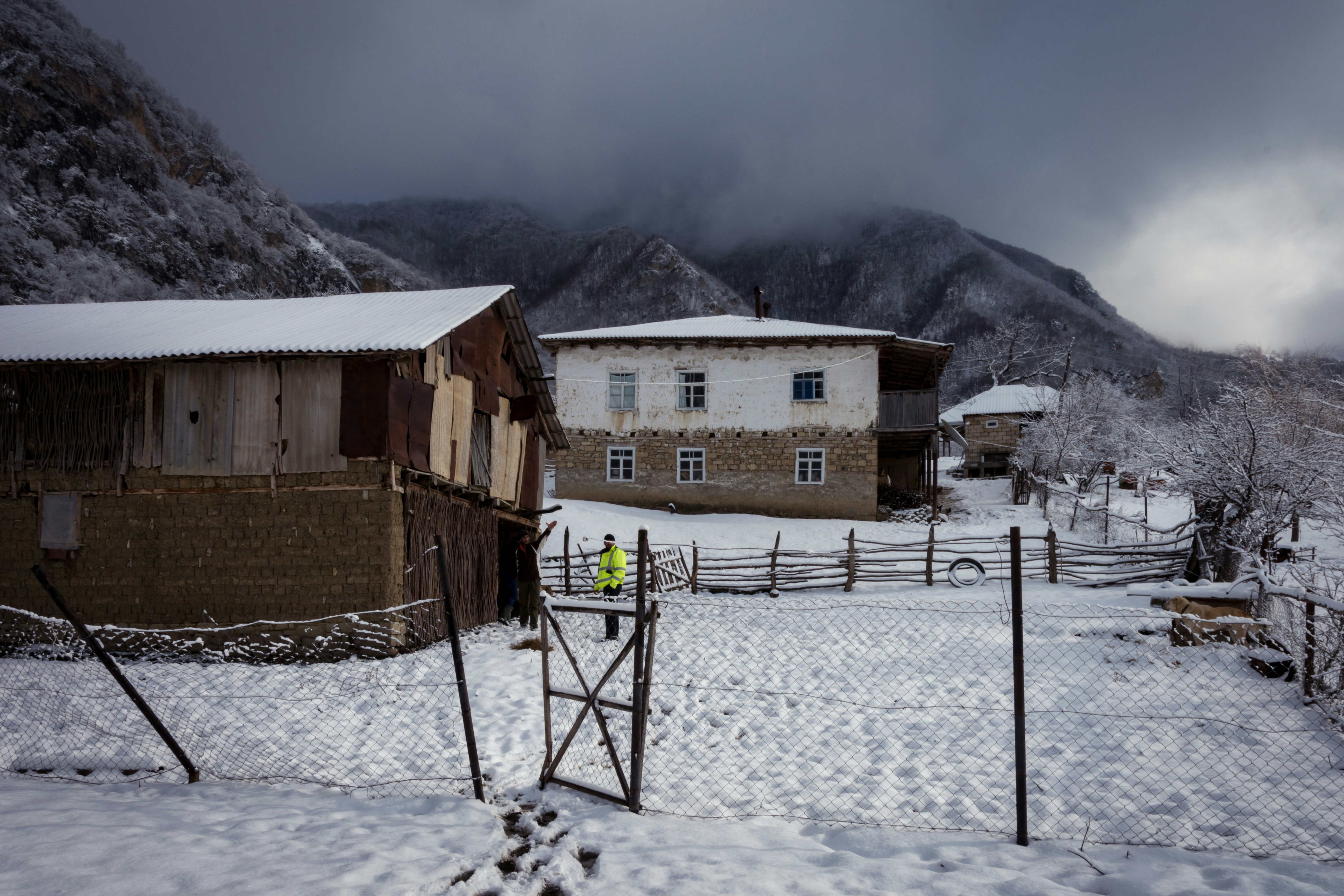 Snow-covered village houses surrounded by misty mountains under a cloudy sky.