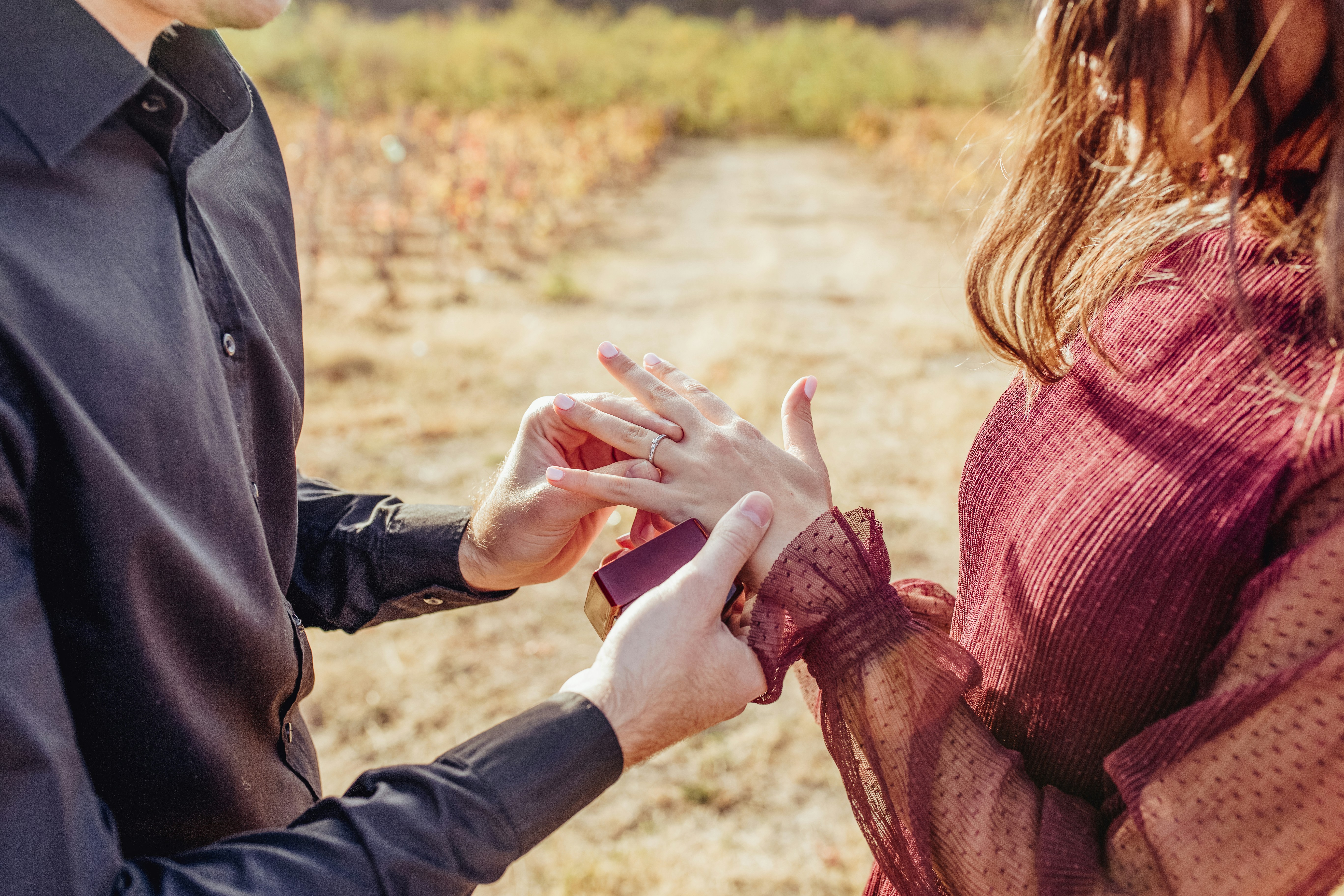 Man placing a ring on a woman's finger in a sunlit field.