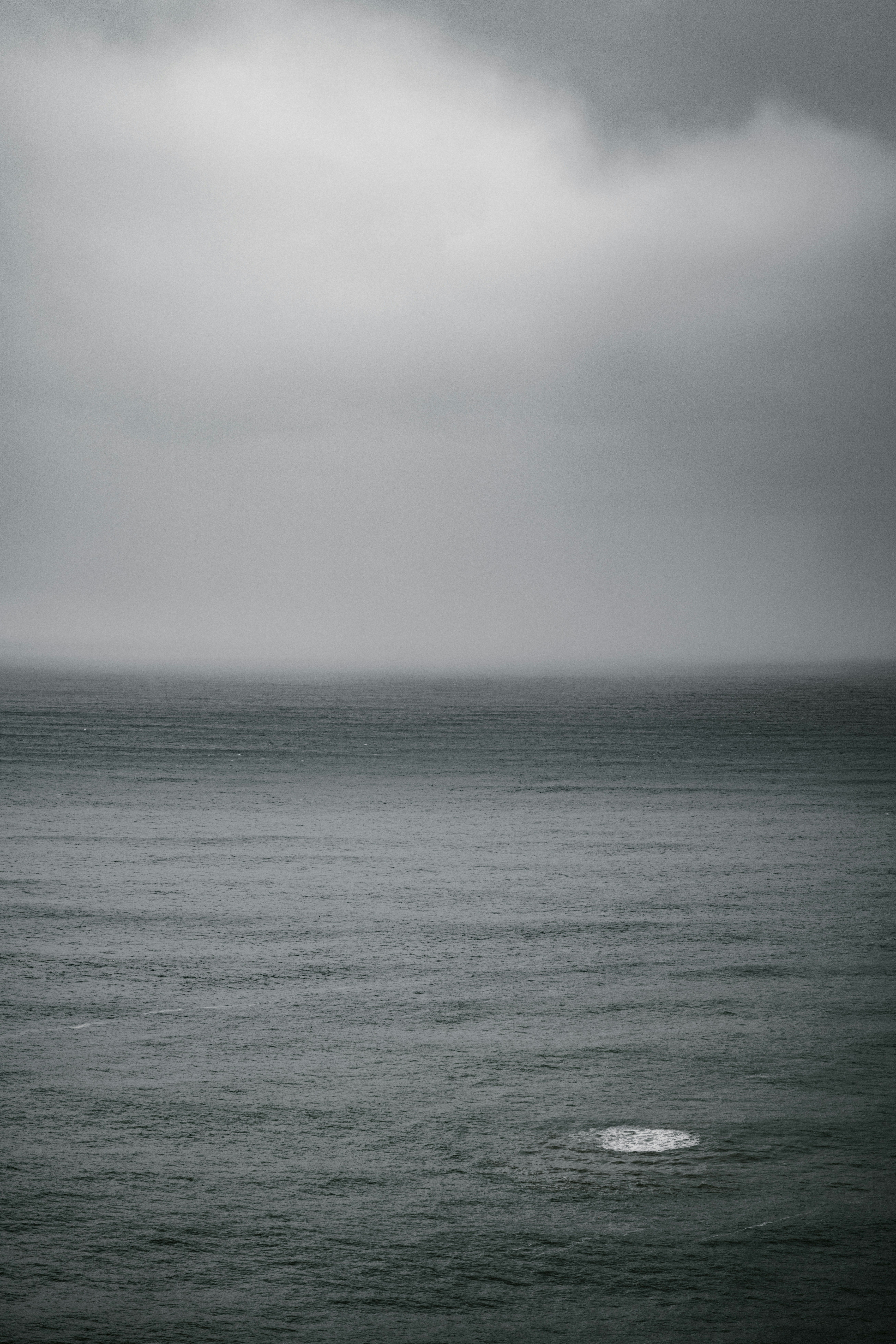 Calm ocean waters under a moody sky, with subtle waves and a distant white froth creating a serene atmosphere.
