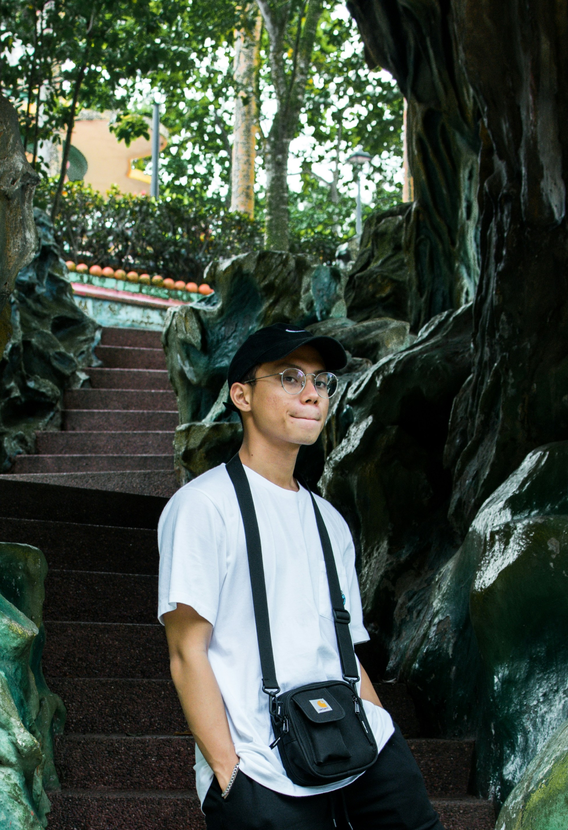 Young man standing on stone steps surrounded by lush greenery and textured rock formations.