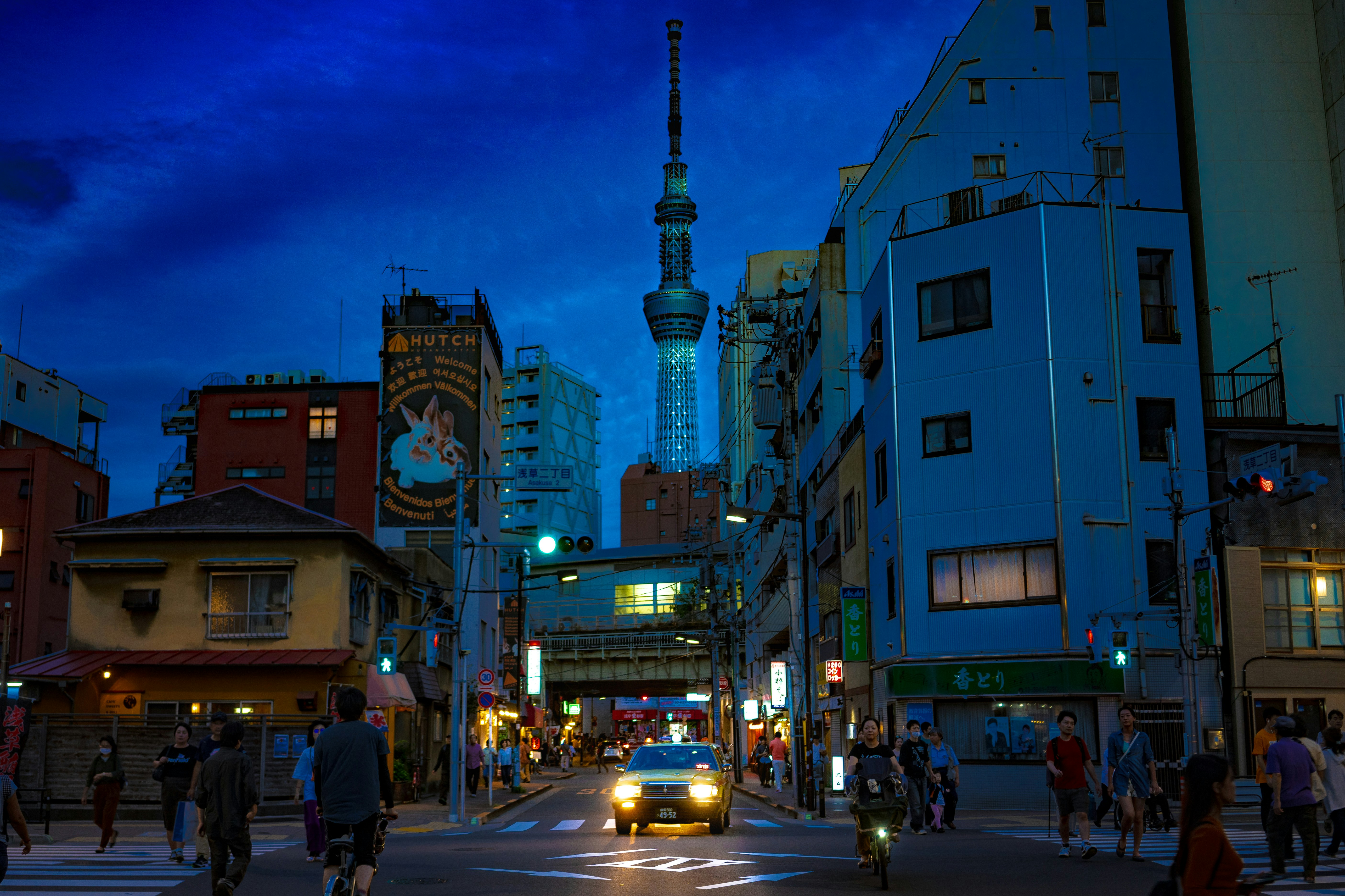 Tokyo's bustling streets illuminated by the iconic Skytree, with a blend of modern and traditional architecture. A yellow taxi navigates through the vibrant scene.