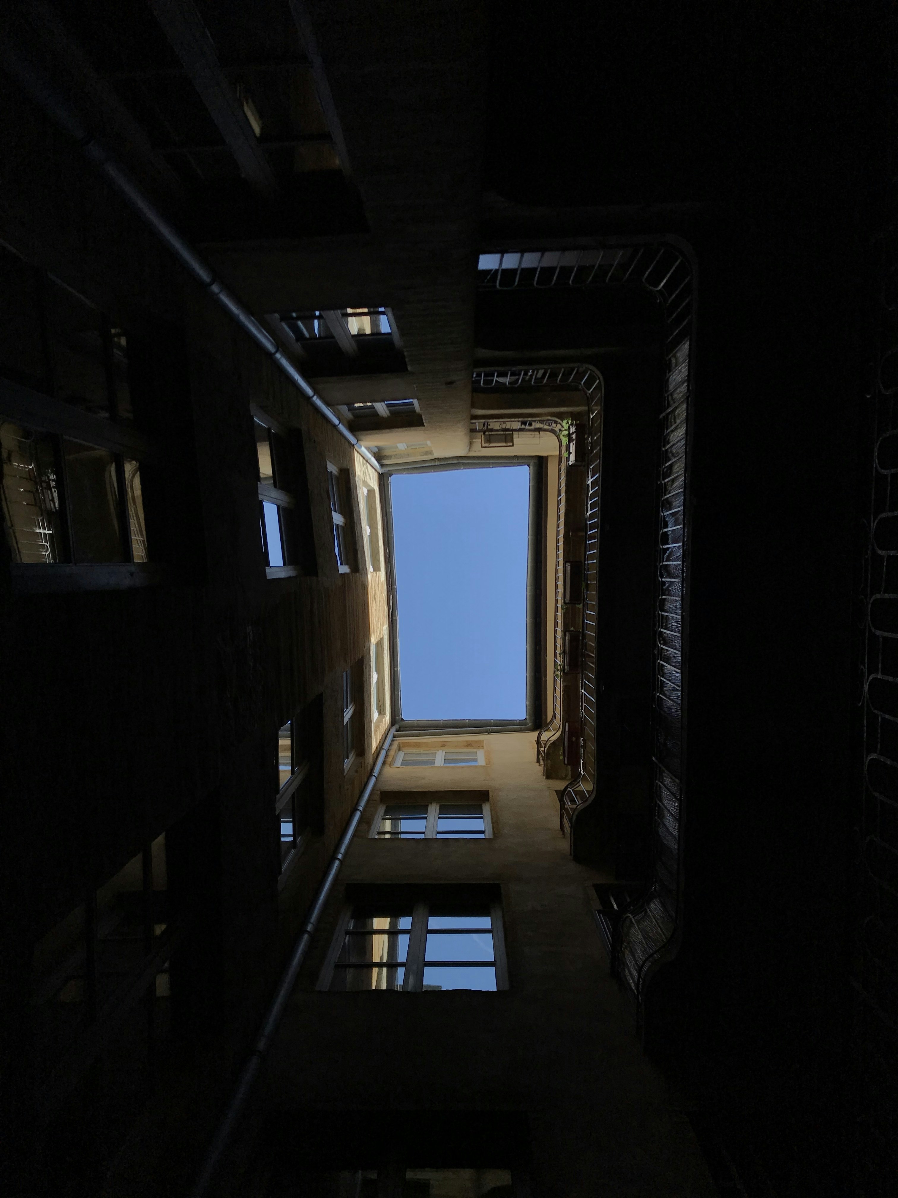 View of a narrow courtyard from below, framed by tall buildings and a clear blue sky above.