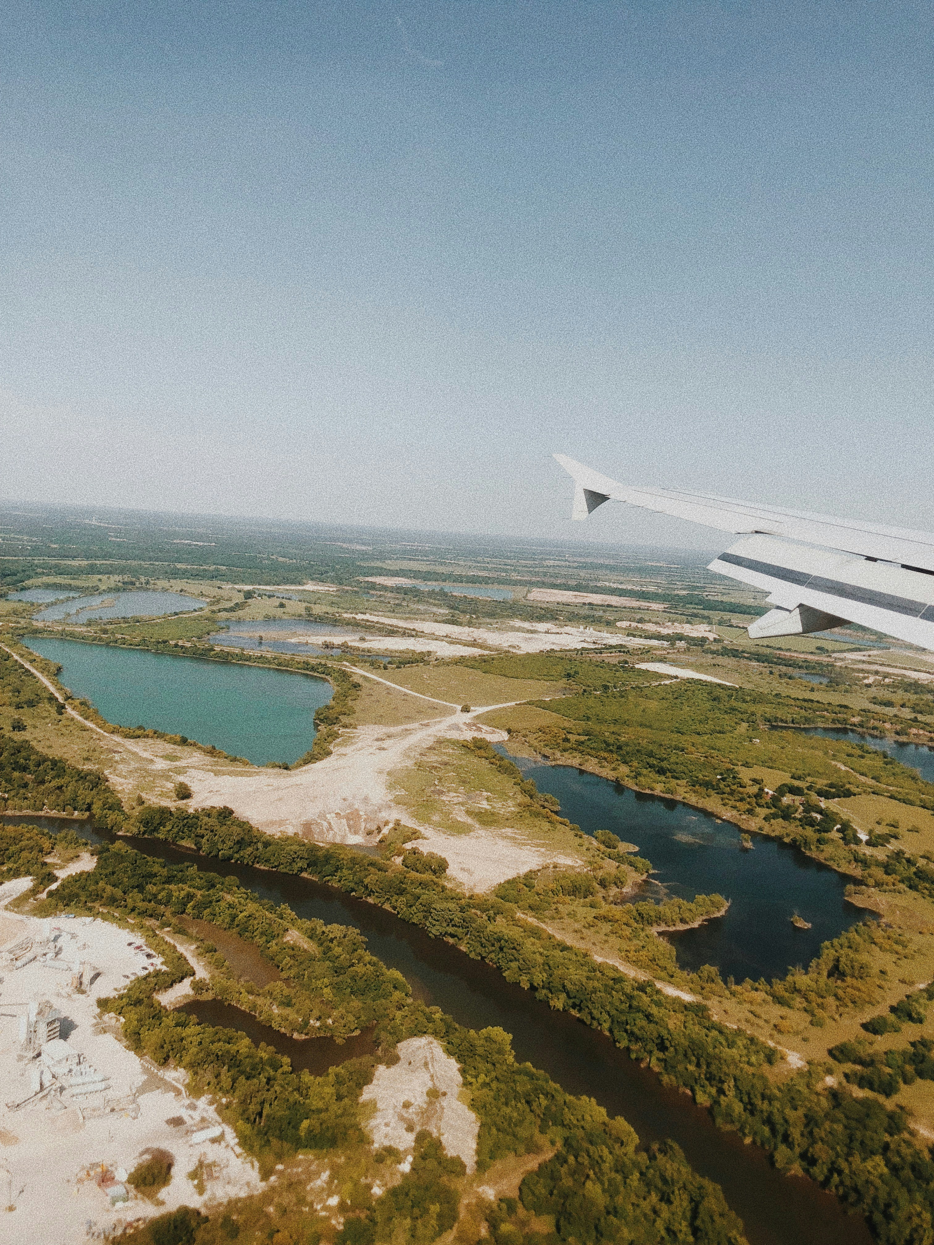 Vibrant blue and green lakes contrast with winding rivers and lush landscapes as seen from an airplane wing. The scene captures the intricate patterns of nature below.