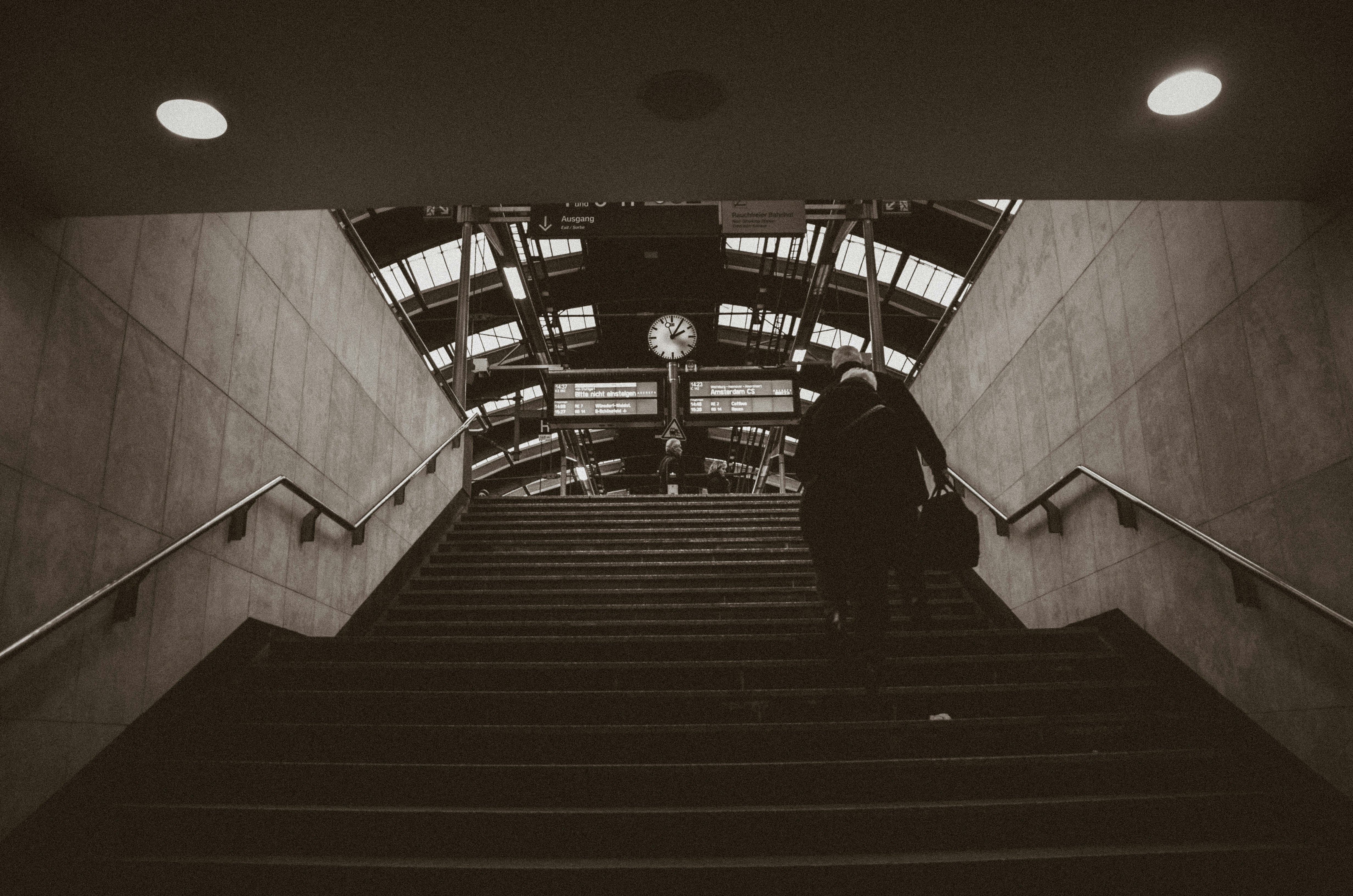 Person ascending stairs towards a clock in a Berlin train station.