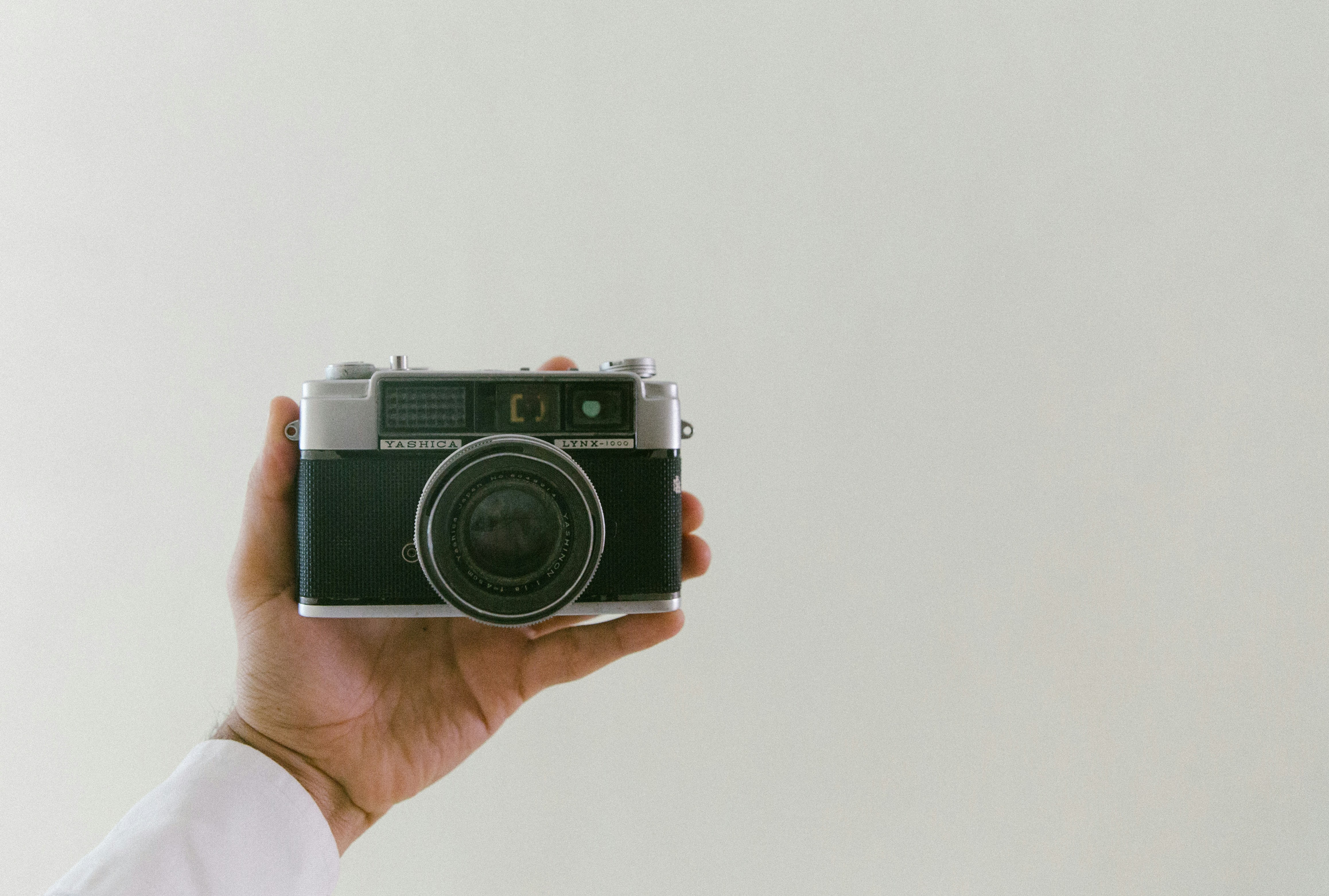 Hand holding a retro-style camera against a minimalist background.