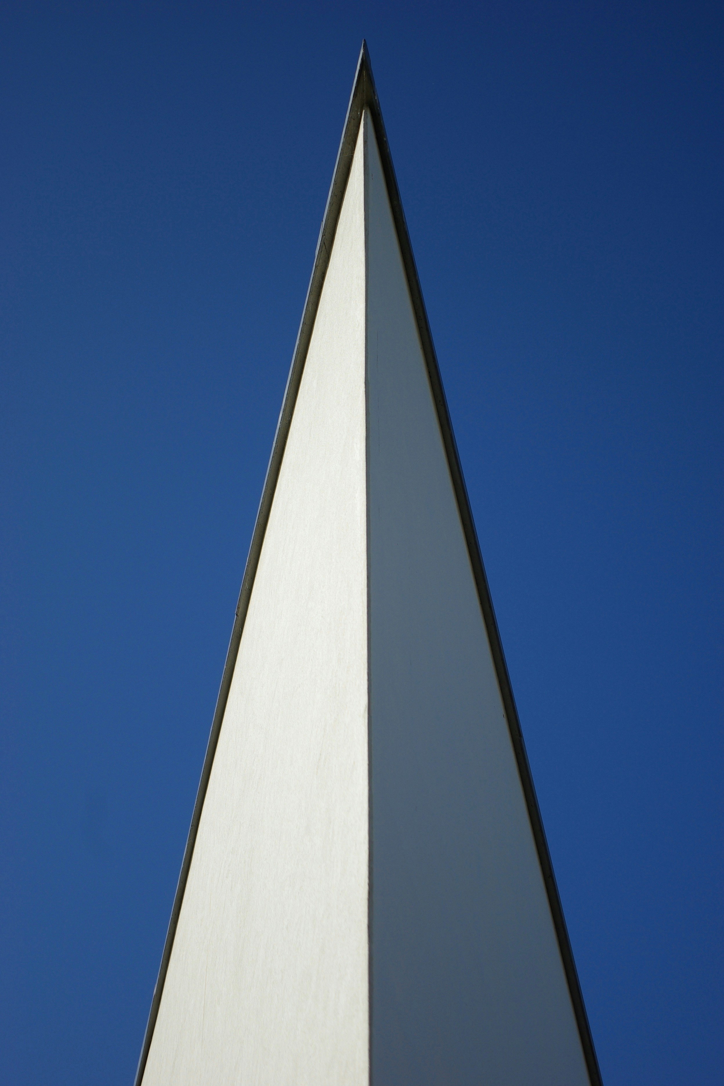 Sharp, white architectural spire reaching towards a clear blue sky, emphasizing simplicity and elegance.