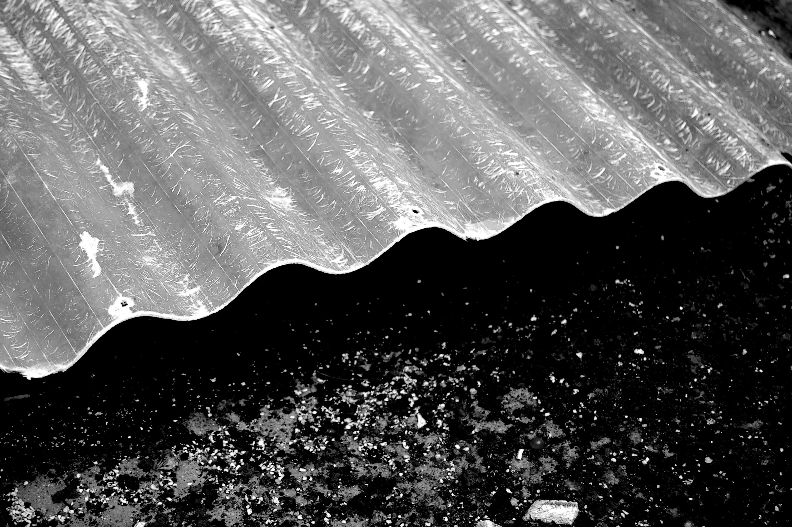 Black and white close-up of a corrugated metal sheet casting rippled shadows on a textured surface.