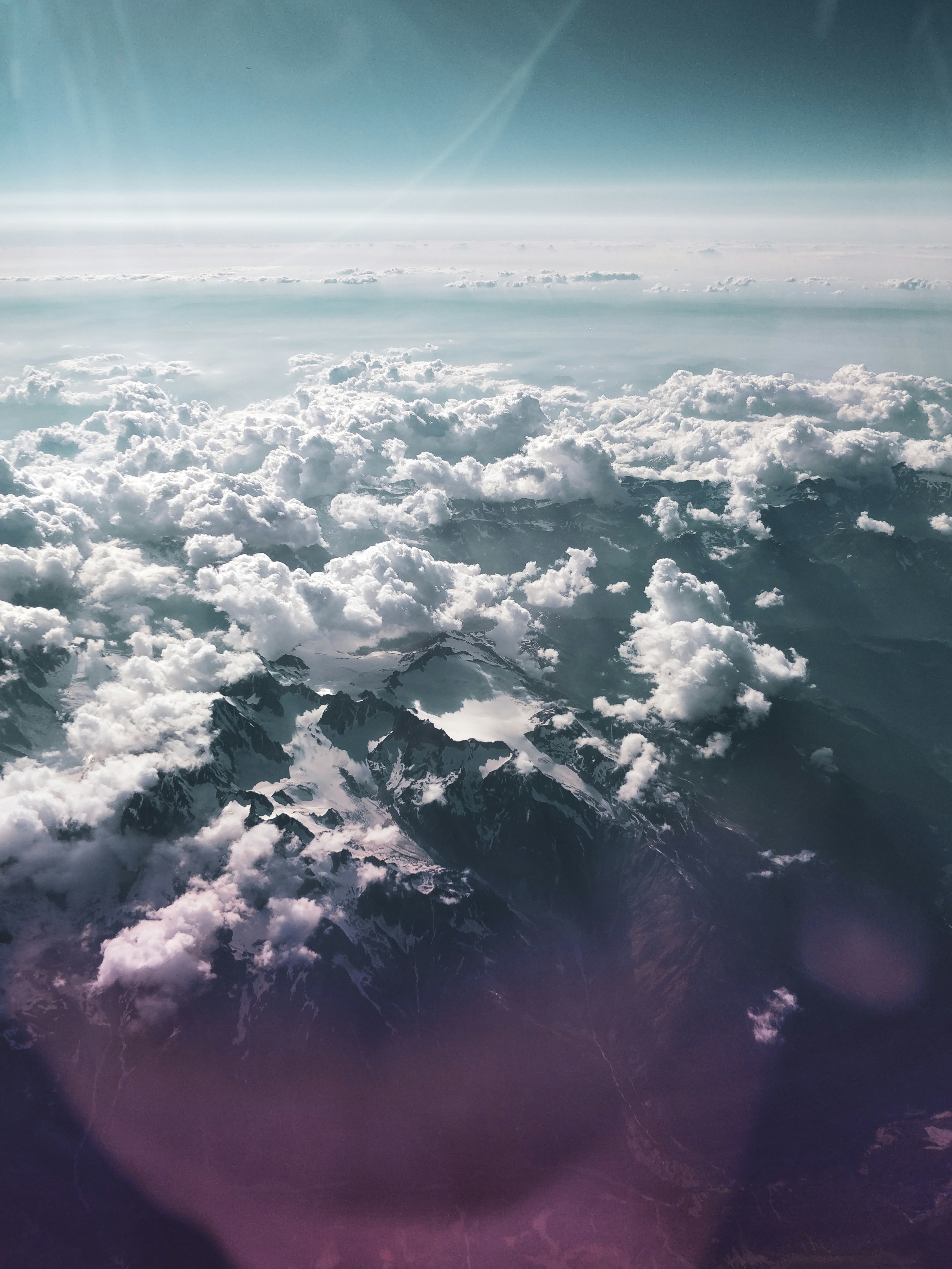 Aerial view of rugged mountains blanketed by dense, fluffy clouds under a serene blue sky.