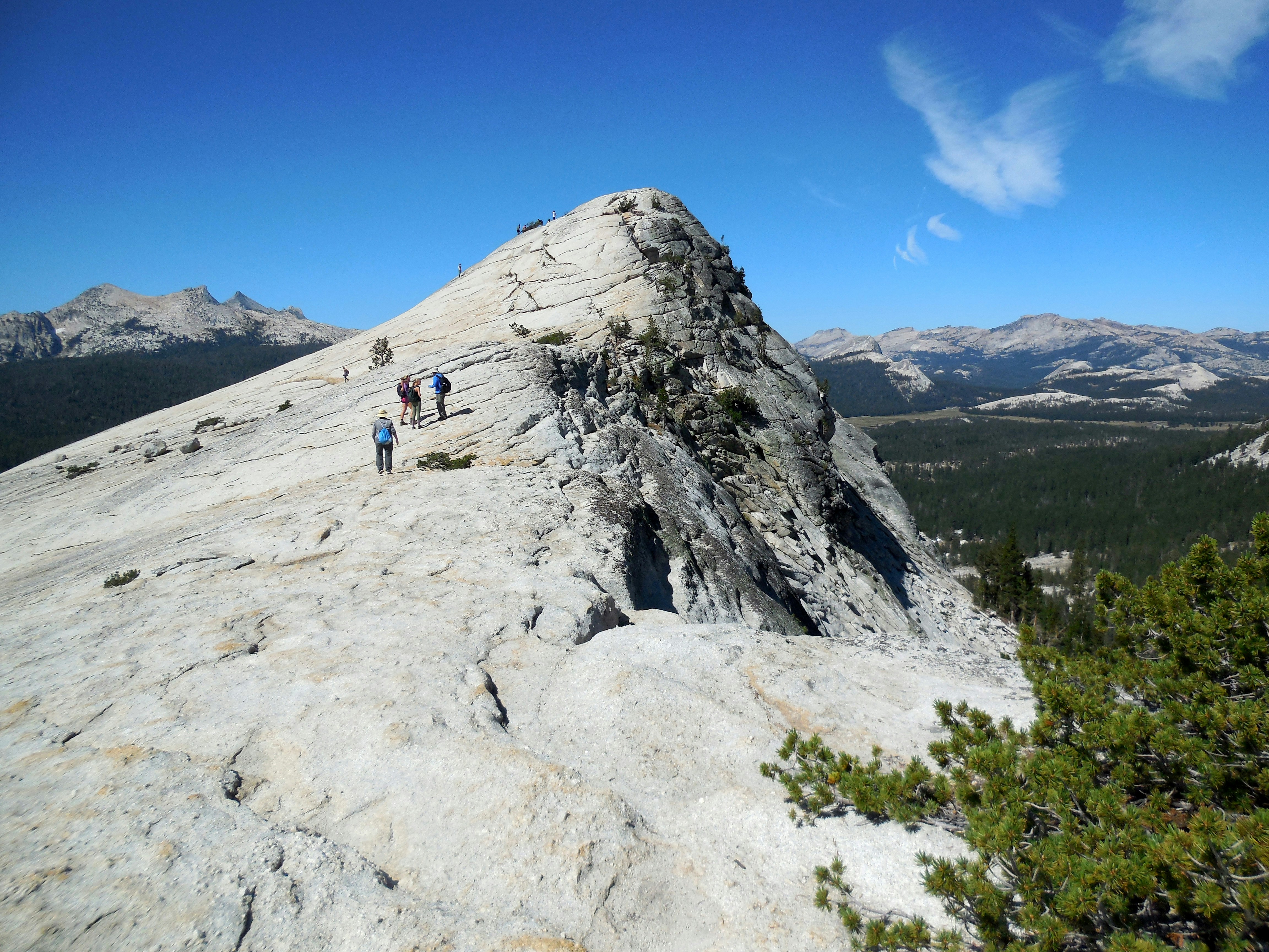 Hikers traverse the rugged surface of Lembert Dome under a clear blue sky in Yosemite National Park.