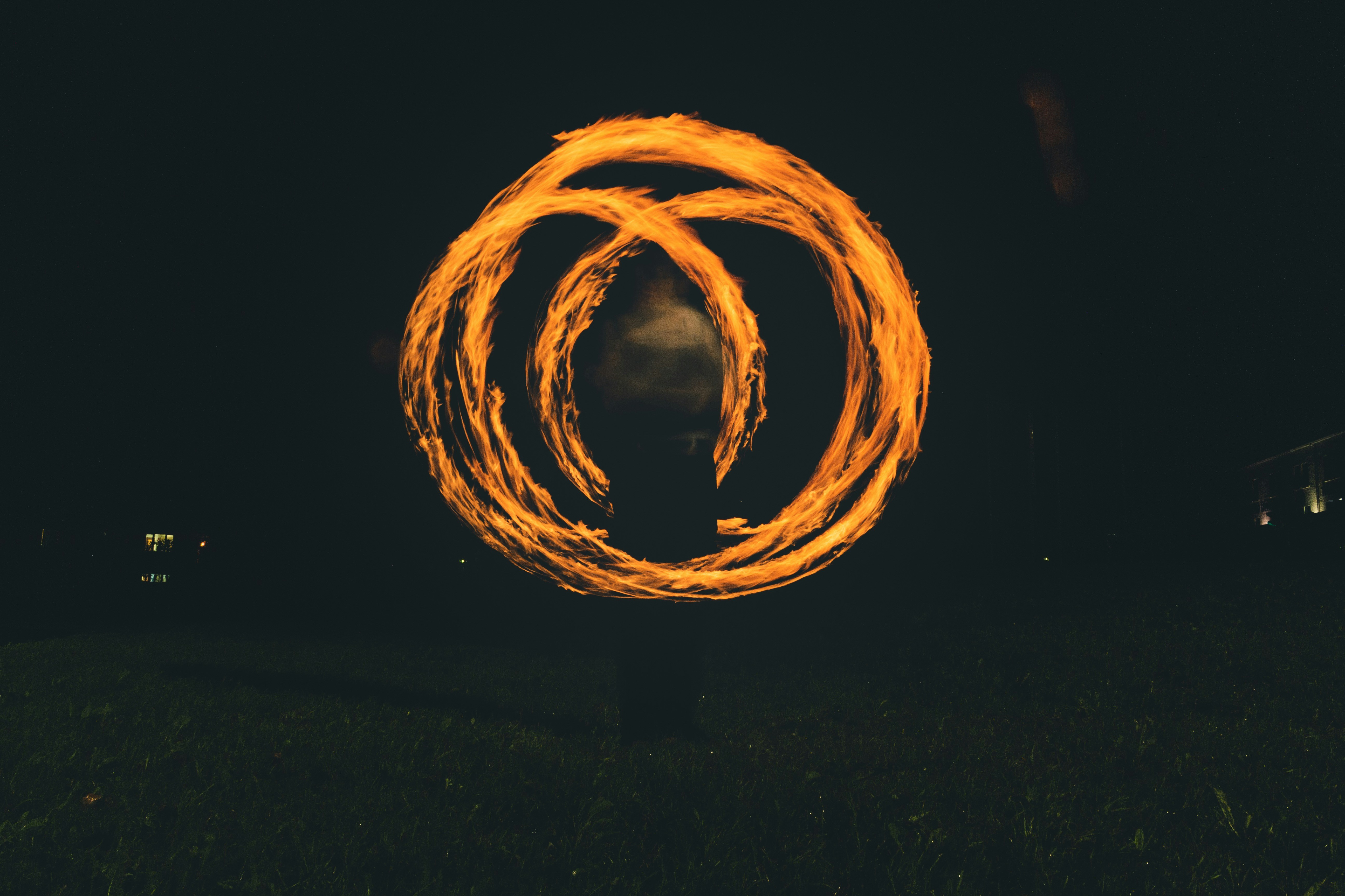 A performer skillfully twirls a flaming staff, creating mesmerizing circular patterns against a dark backdrop.