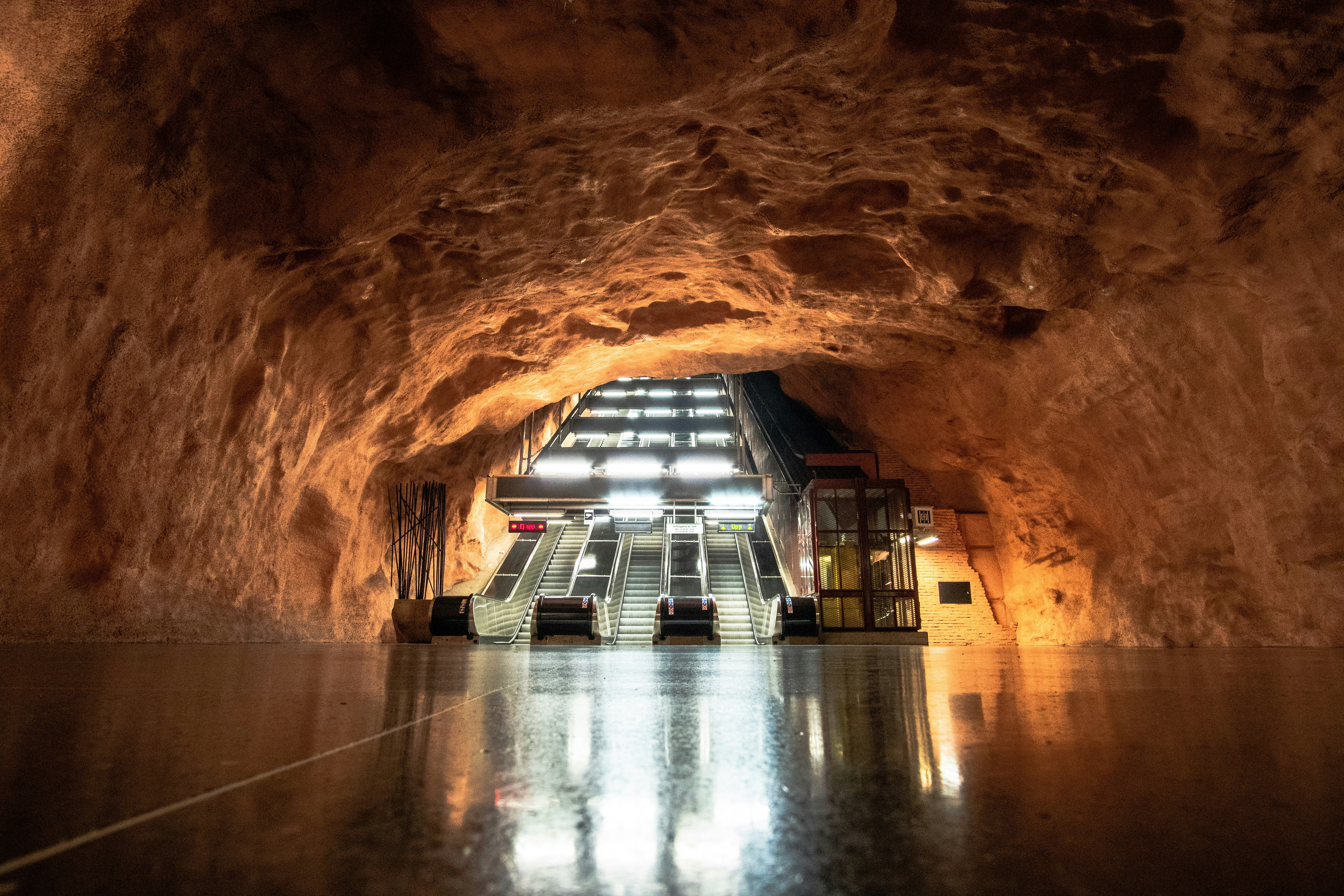 Modern escalator leading into an expansive, illuminated cave with rocky walls.