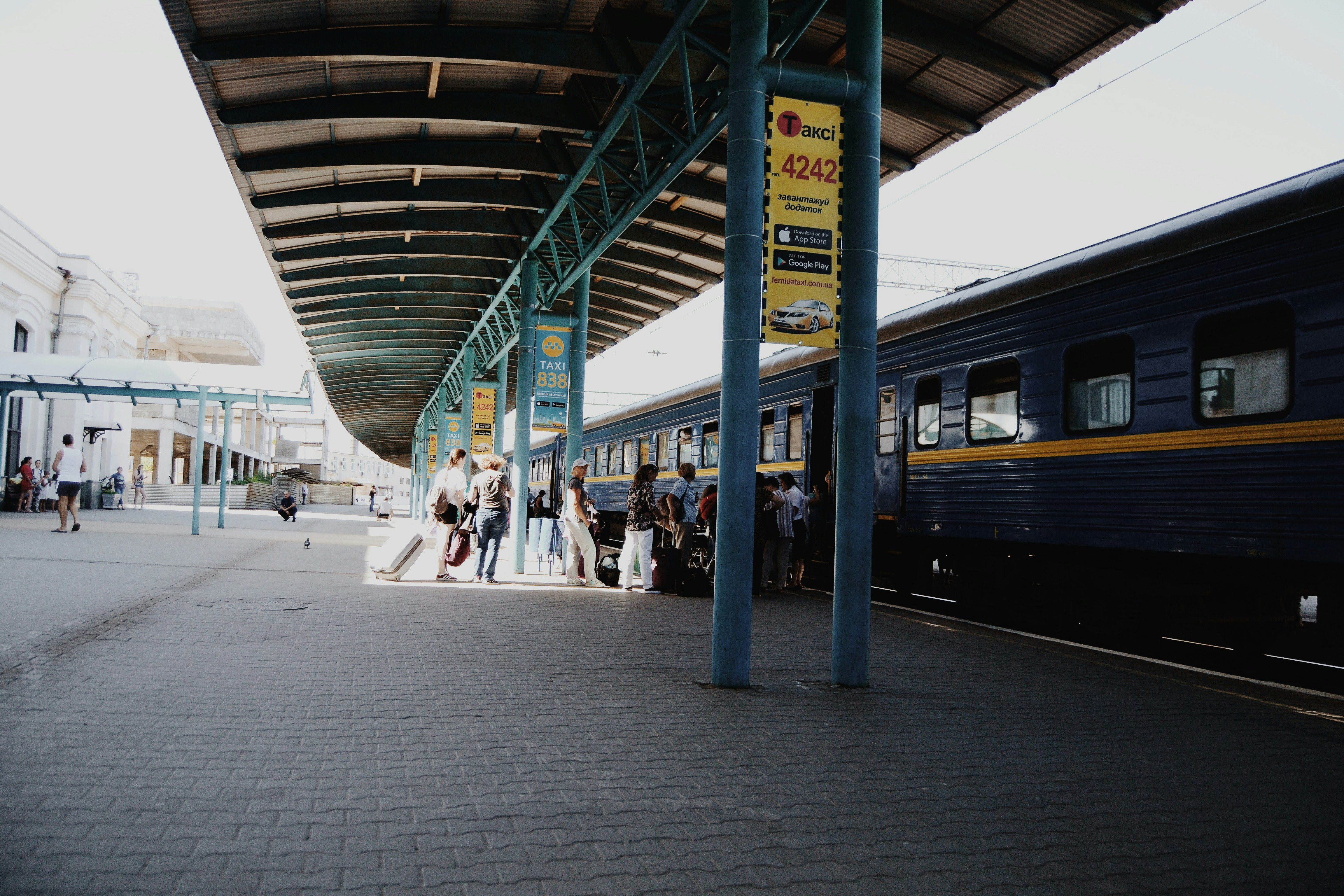 People gather on a train platform beside a blue train under a covered structure.